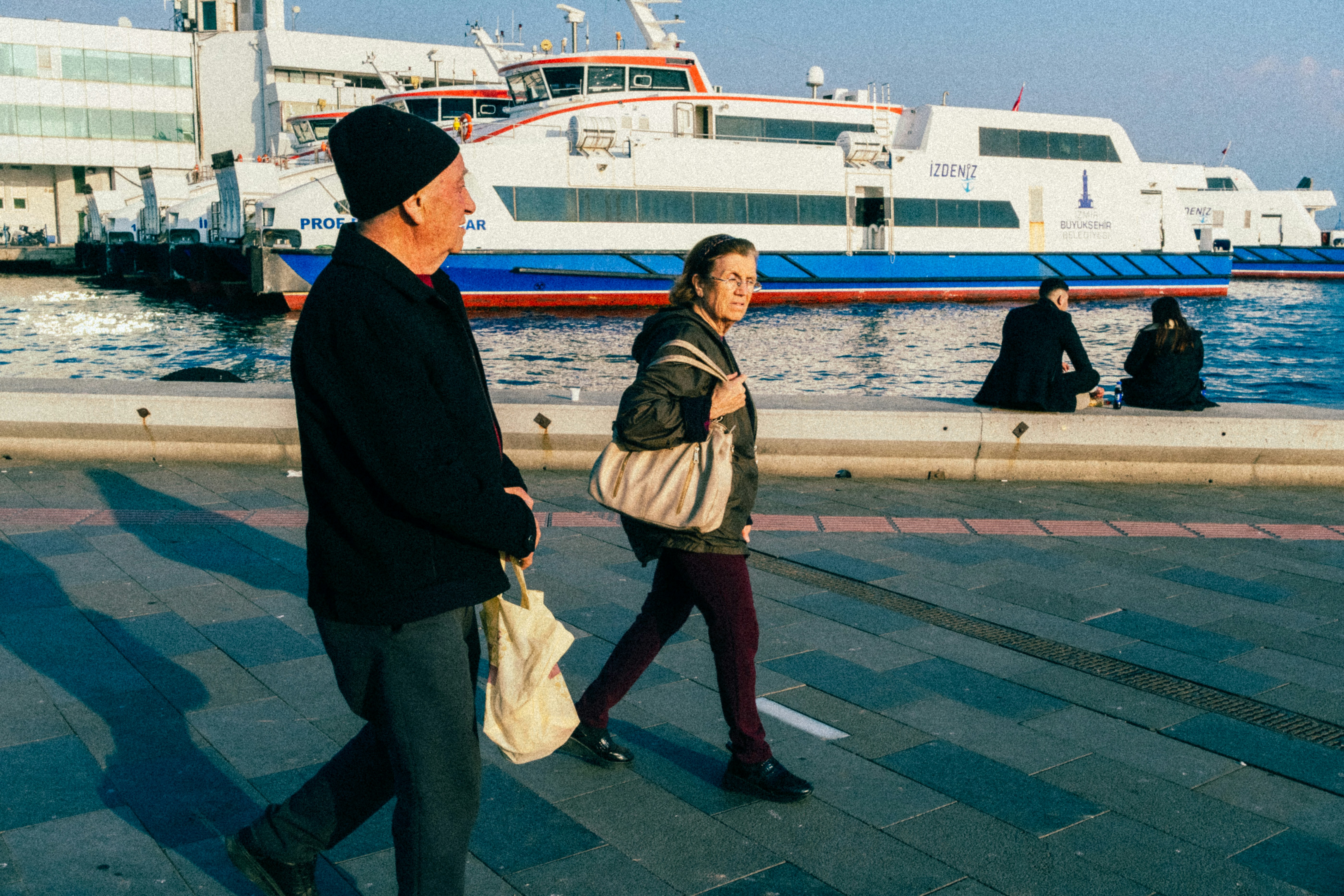 Stroll by the Ferry: Two Walkers and a Dockside Wake