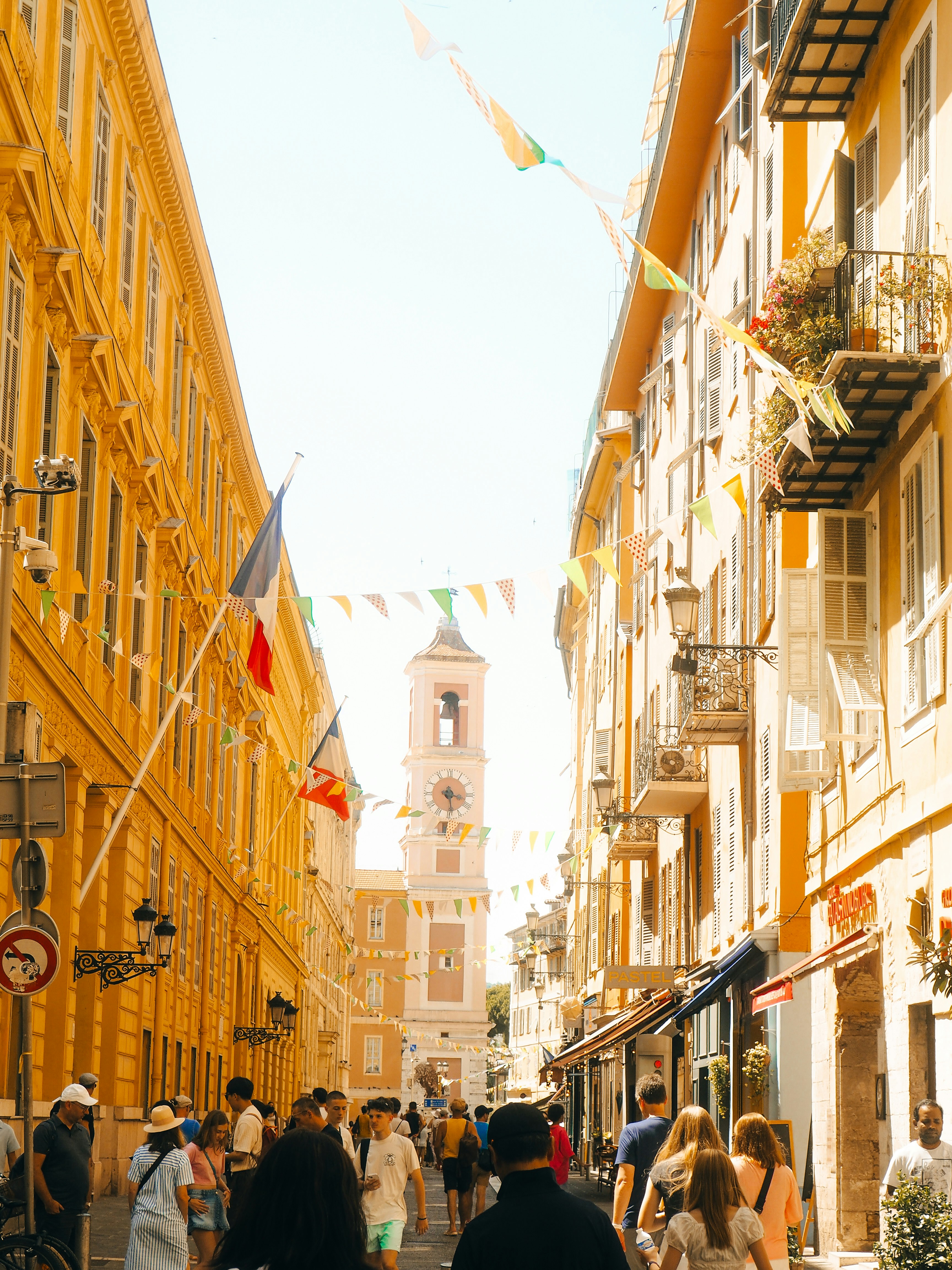 Sunlit Calle: Flags, Shadows, and a Clock Tower Bias