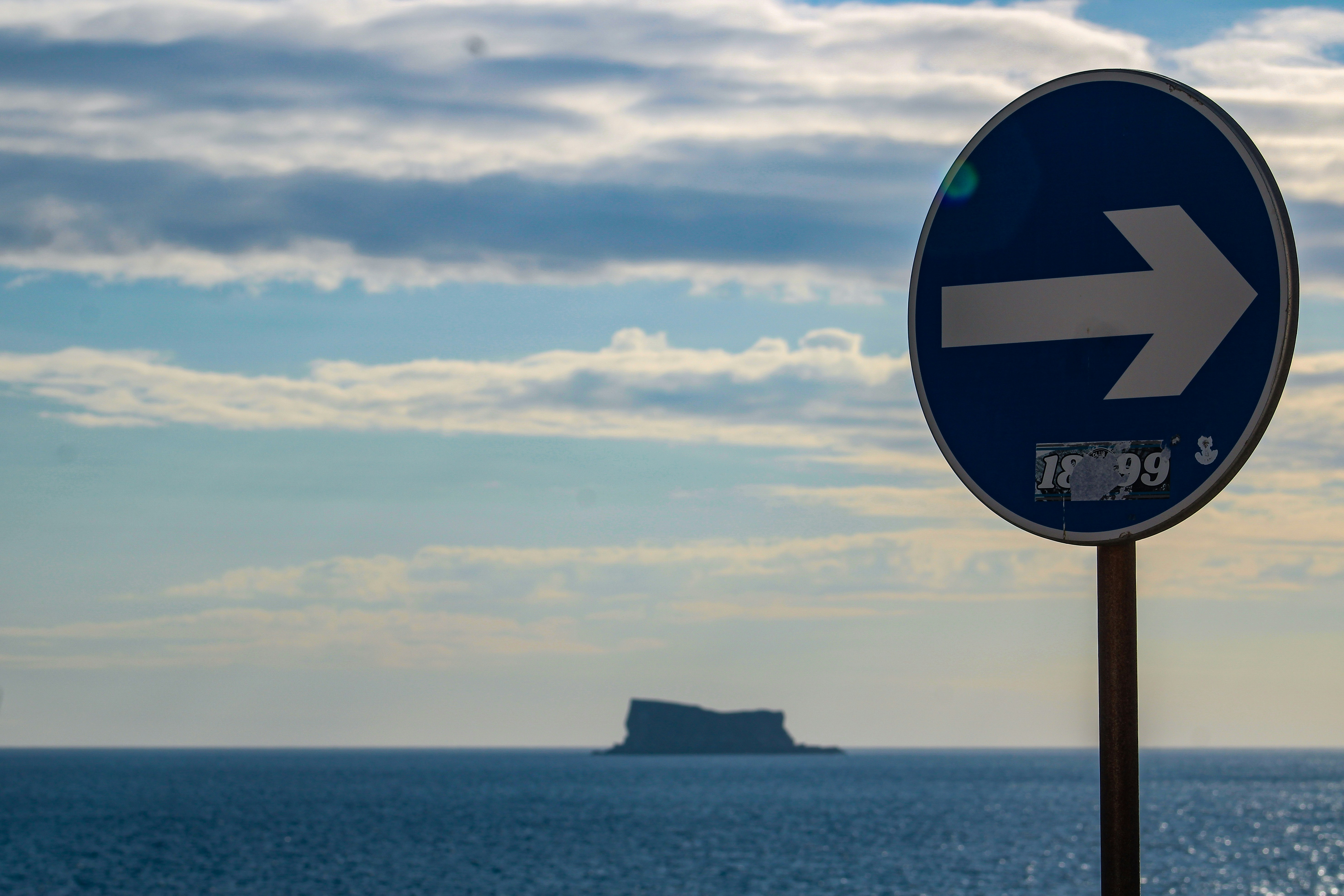 Arrow Sign Overlooking a Seascape: A Quiet Sea Horizon with a Dark Island