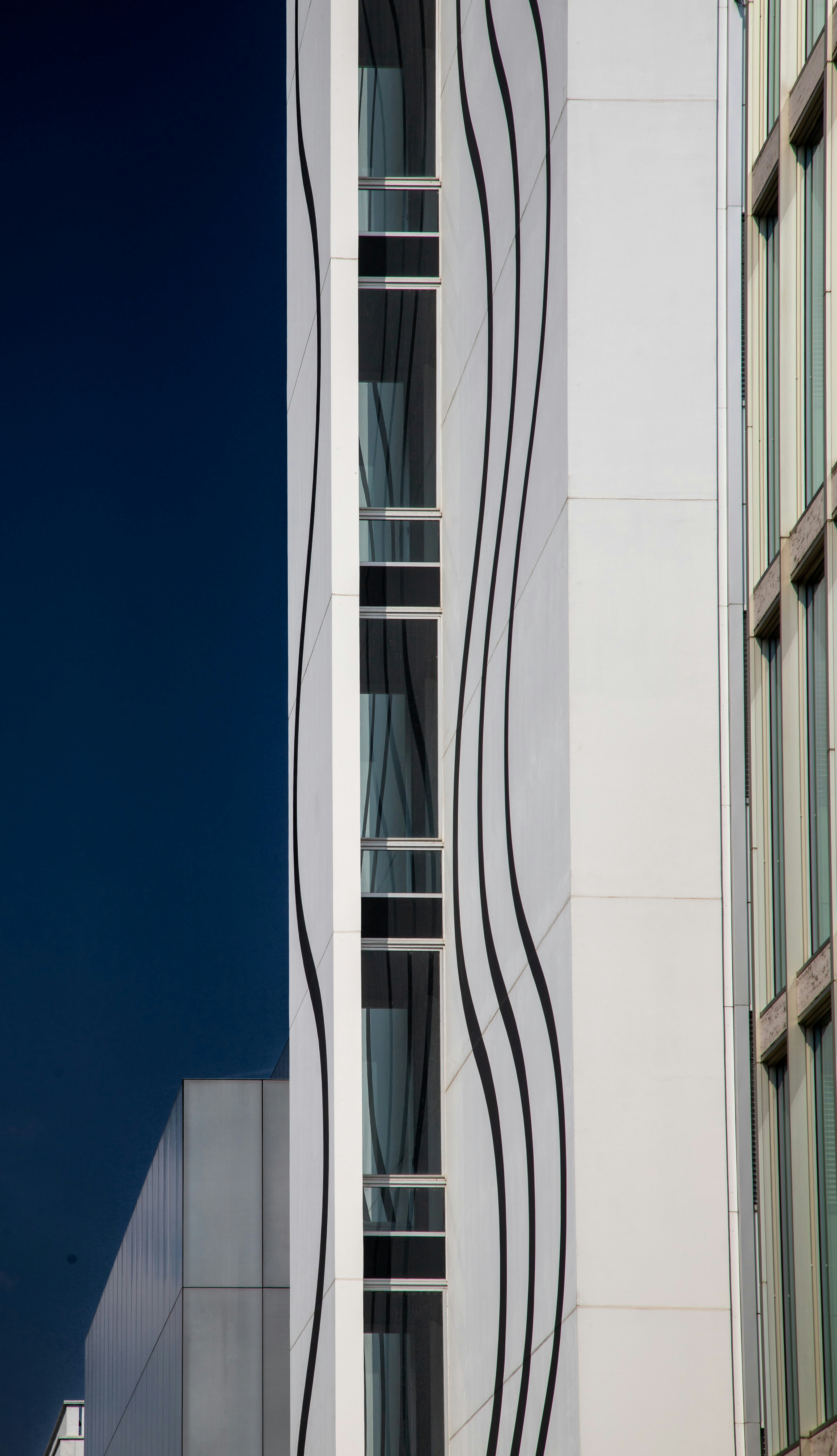 Wavy lines on a white façade: a vertical study of architecture and shadow
