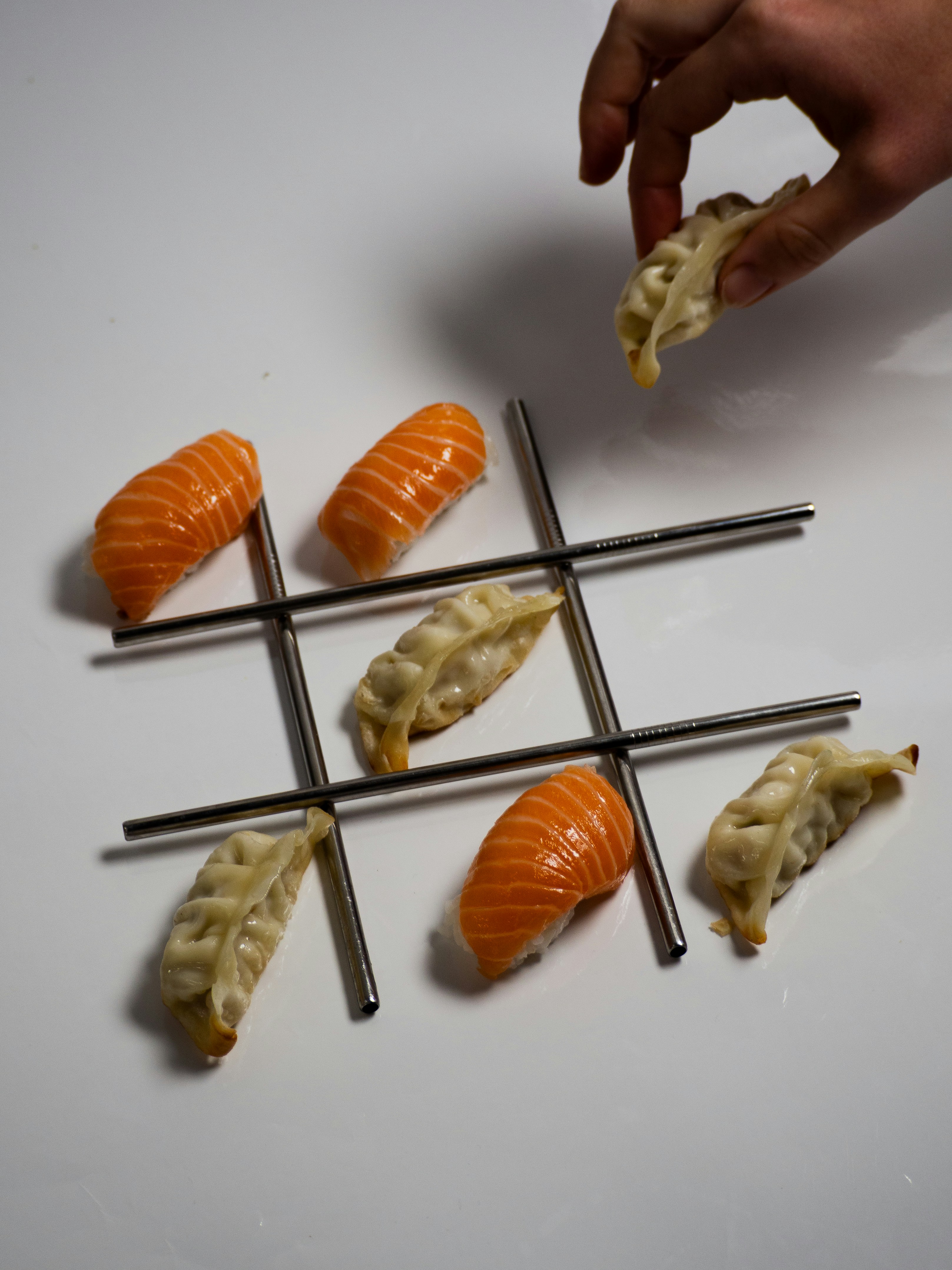Strategic Sushi Grid: Salmon Nigiri and Dumpling Pieces Hover Over a Modern Tic-Tac-Toe