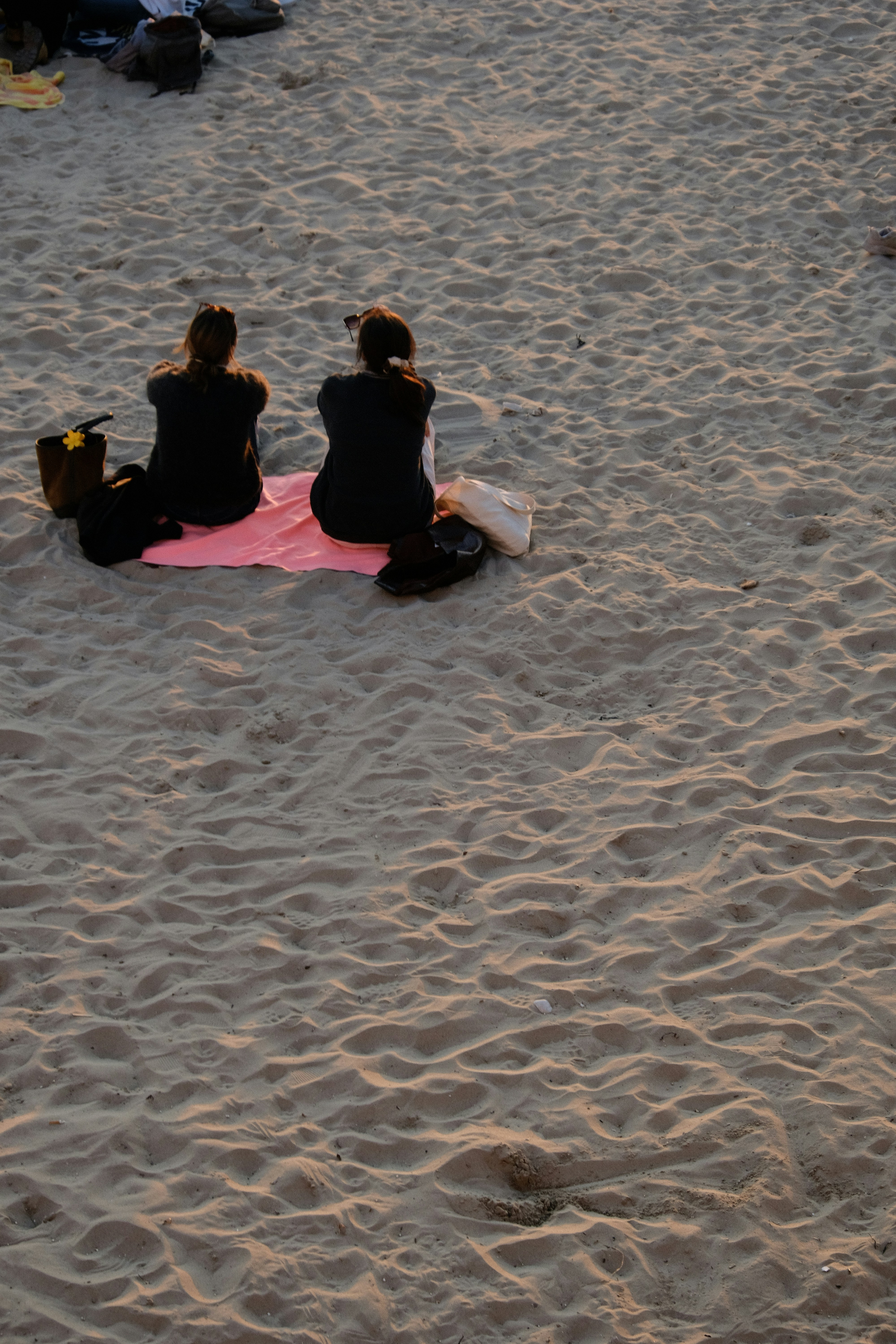 Two friends on a pink blanket share a quiet moment on sunlit sand