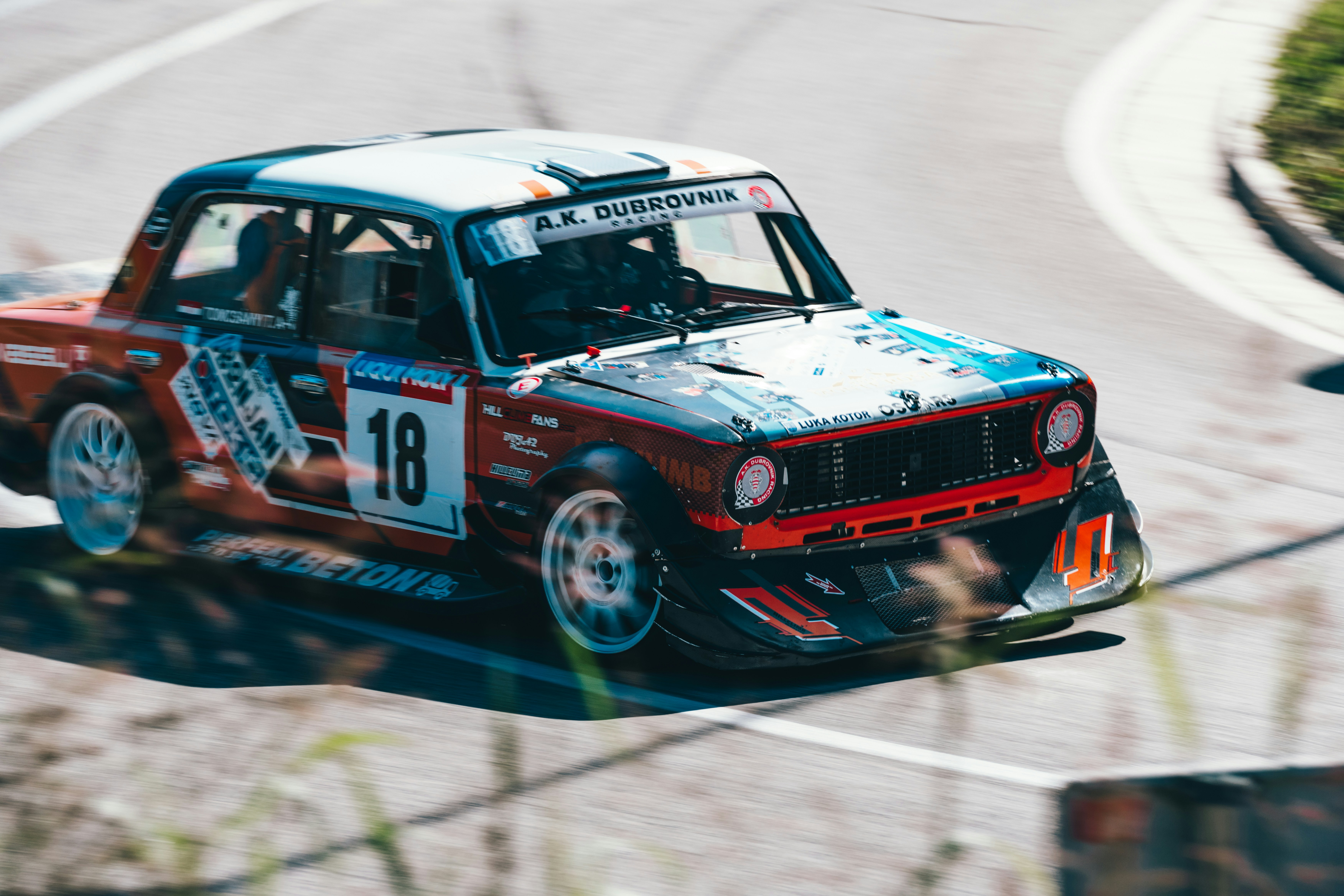 Blue race car with orange accents rails through a sunlit track