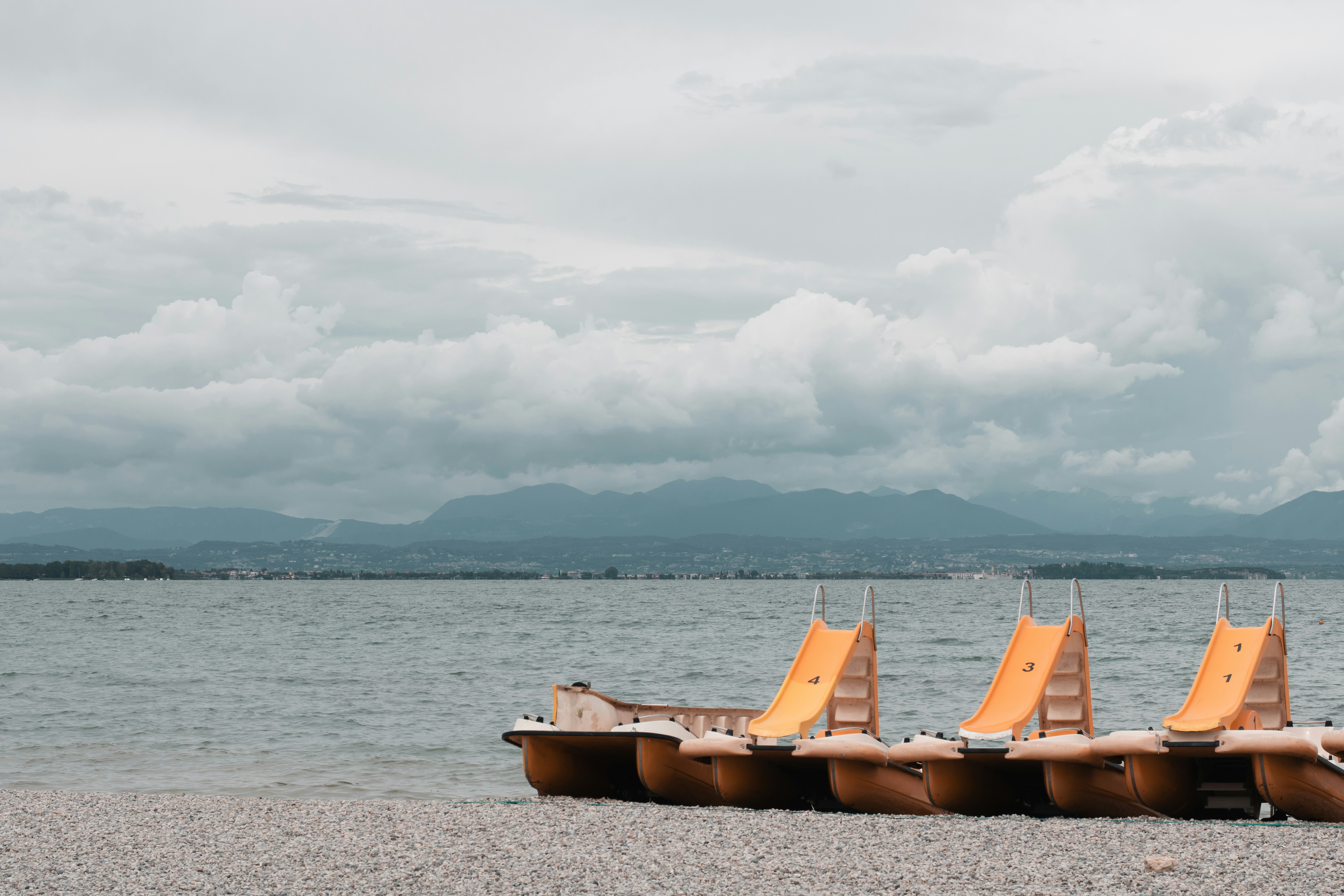 Orange Boats Rest on Pebbled Shore Under Quiet Clouds