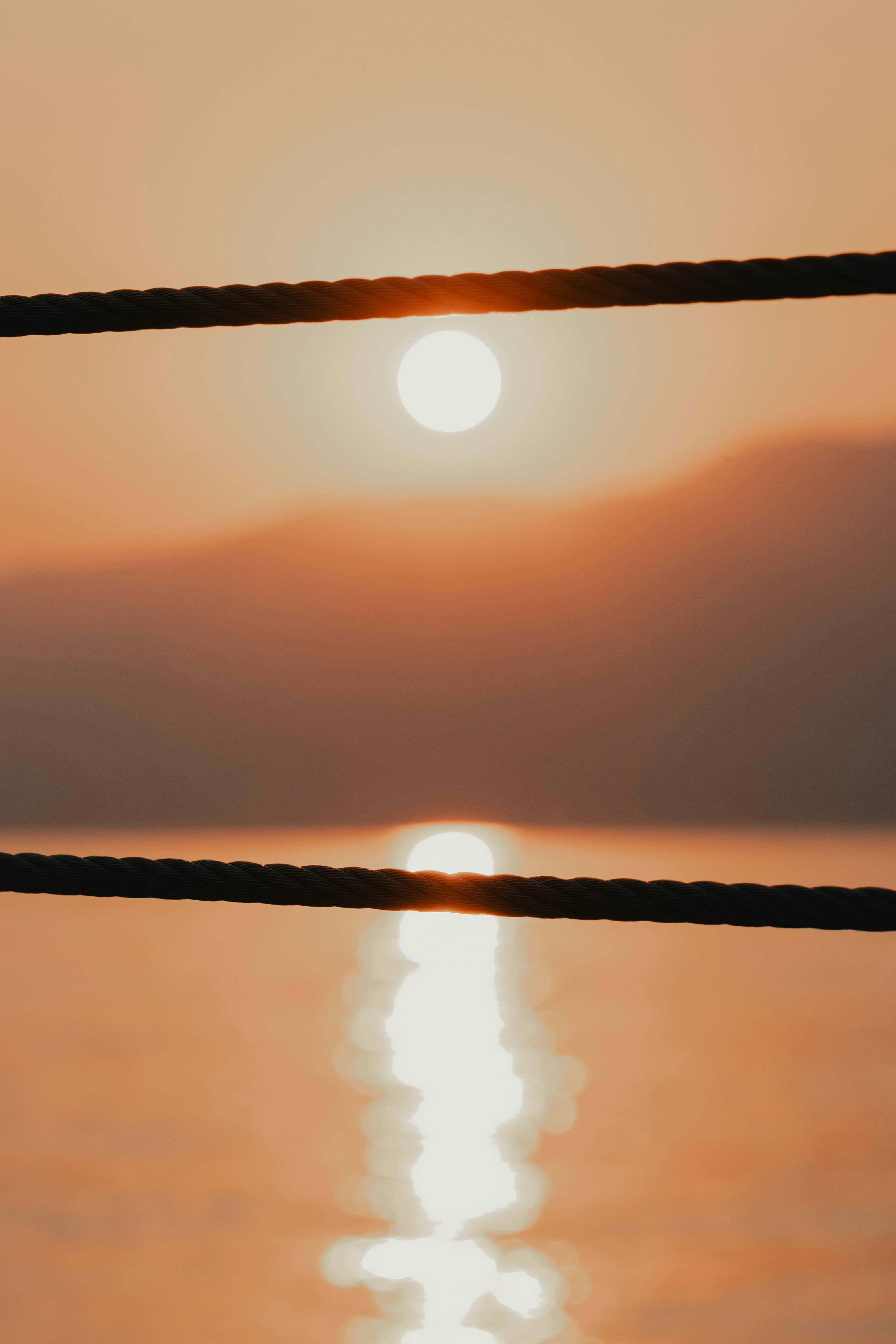 Sunset Between Cables: Orange Haze Over Quiet Water