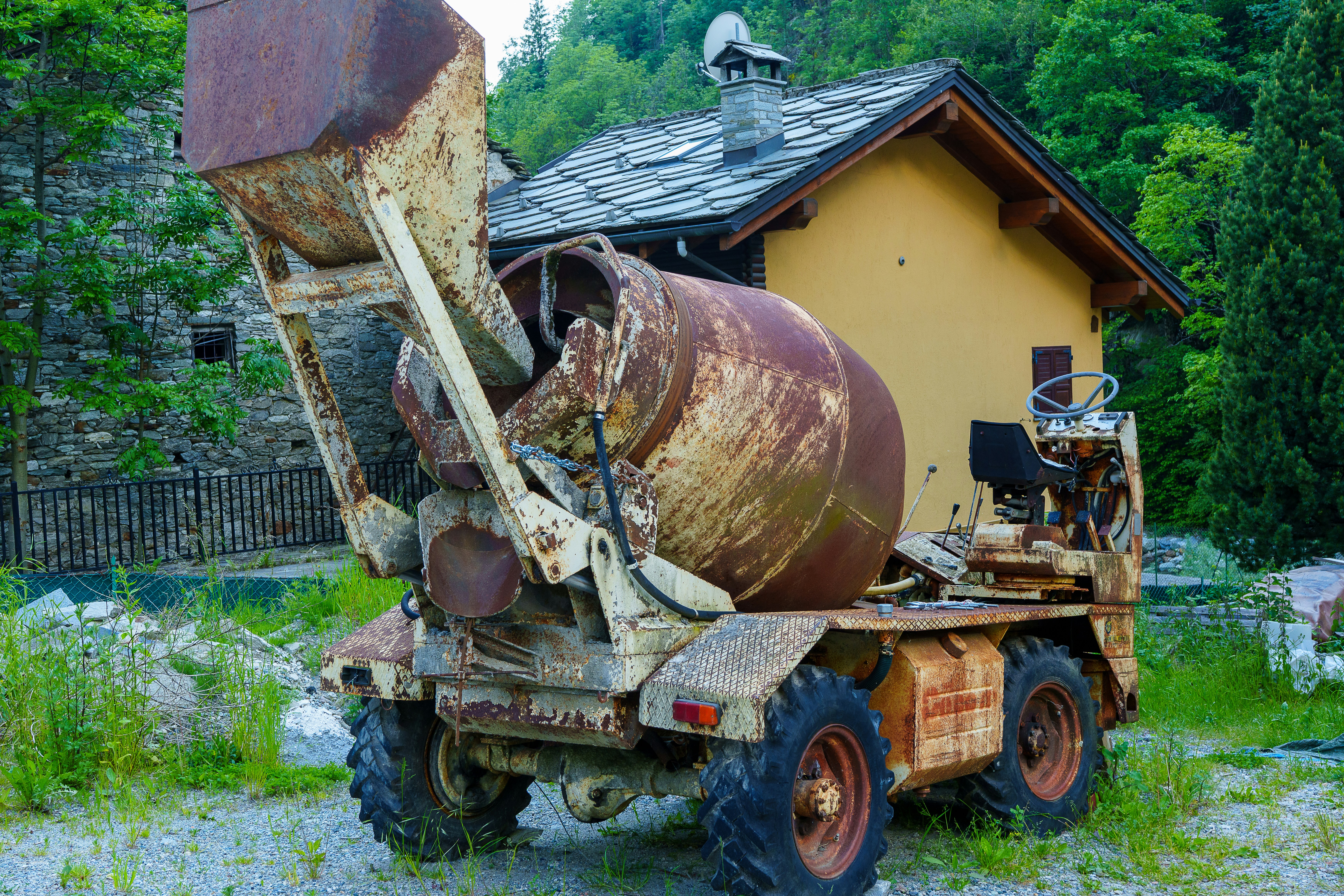 Rusty Mixer on the Verge of Green: A Weathered Workhorse in a Quiet Mountain Yard