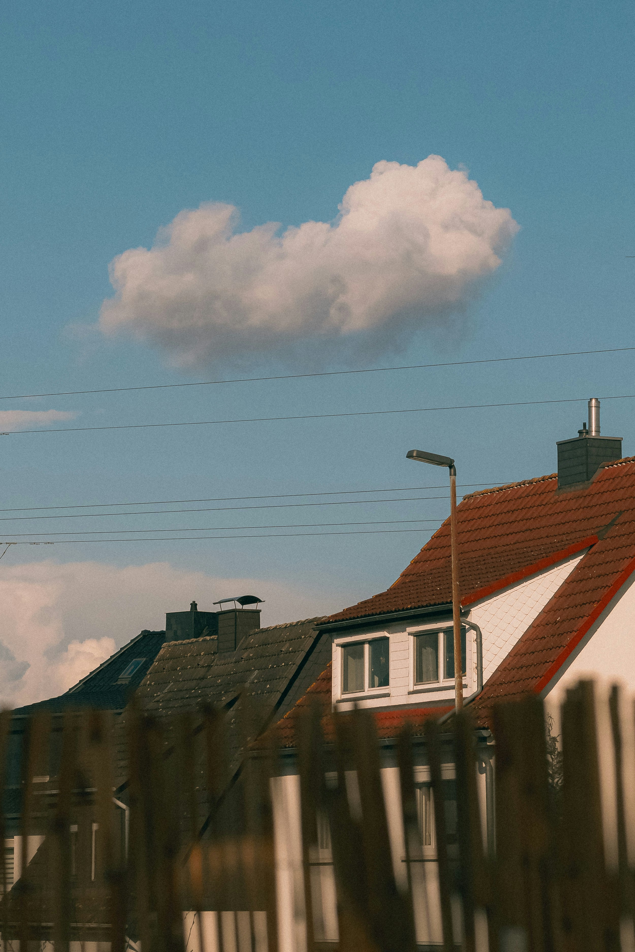 Urban Sky: Cloud, Rooftop, and Cable Lines Over a Quiet Suburban Fence