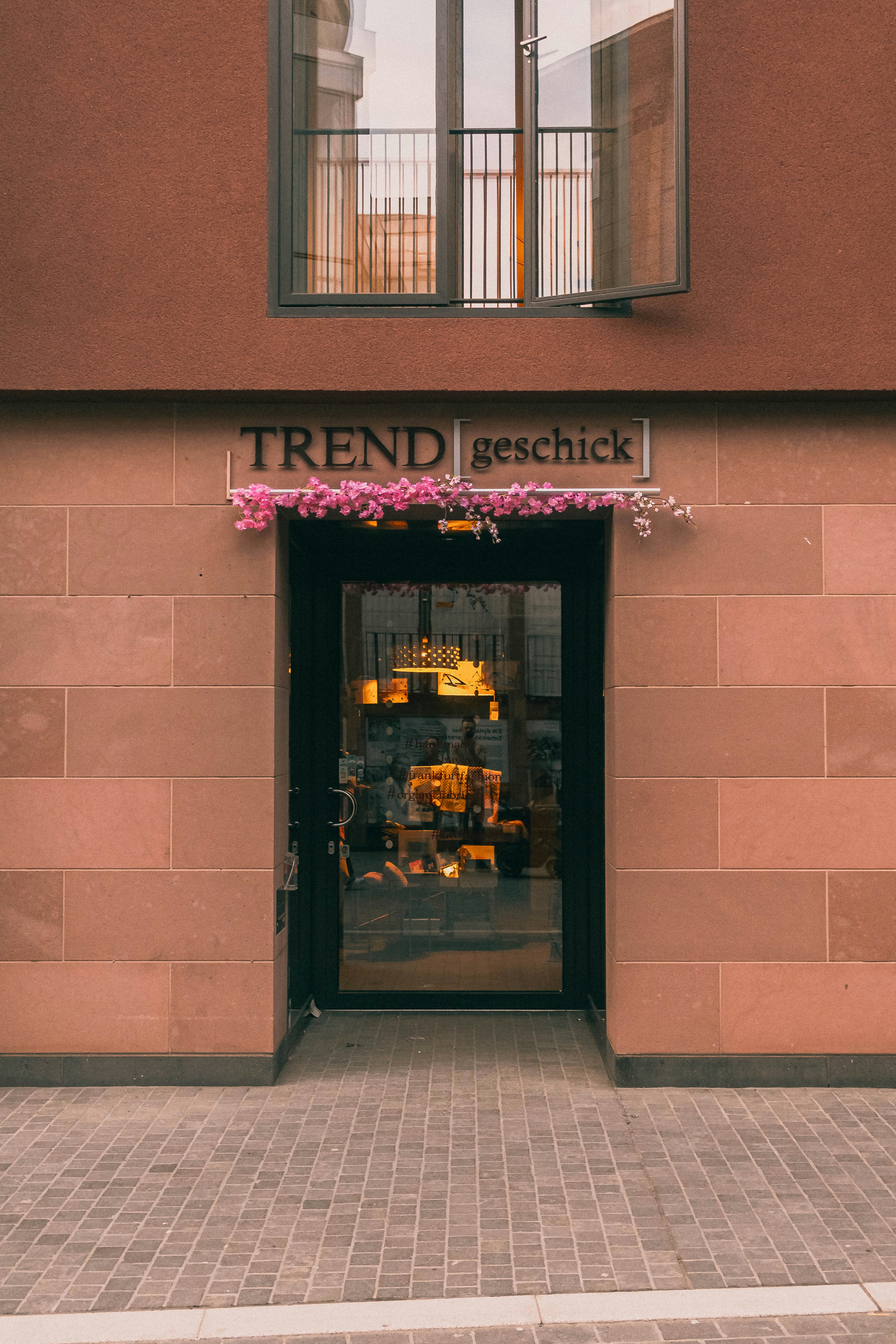 Shopfront of Trend Gescheick: Pink Flowers Framing a Dark Entrance