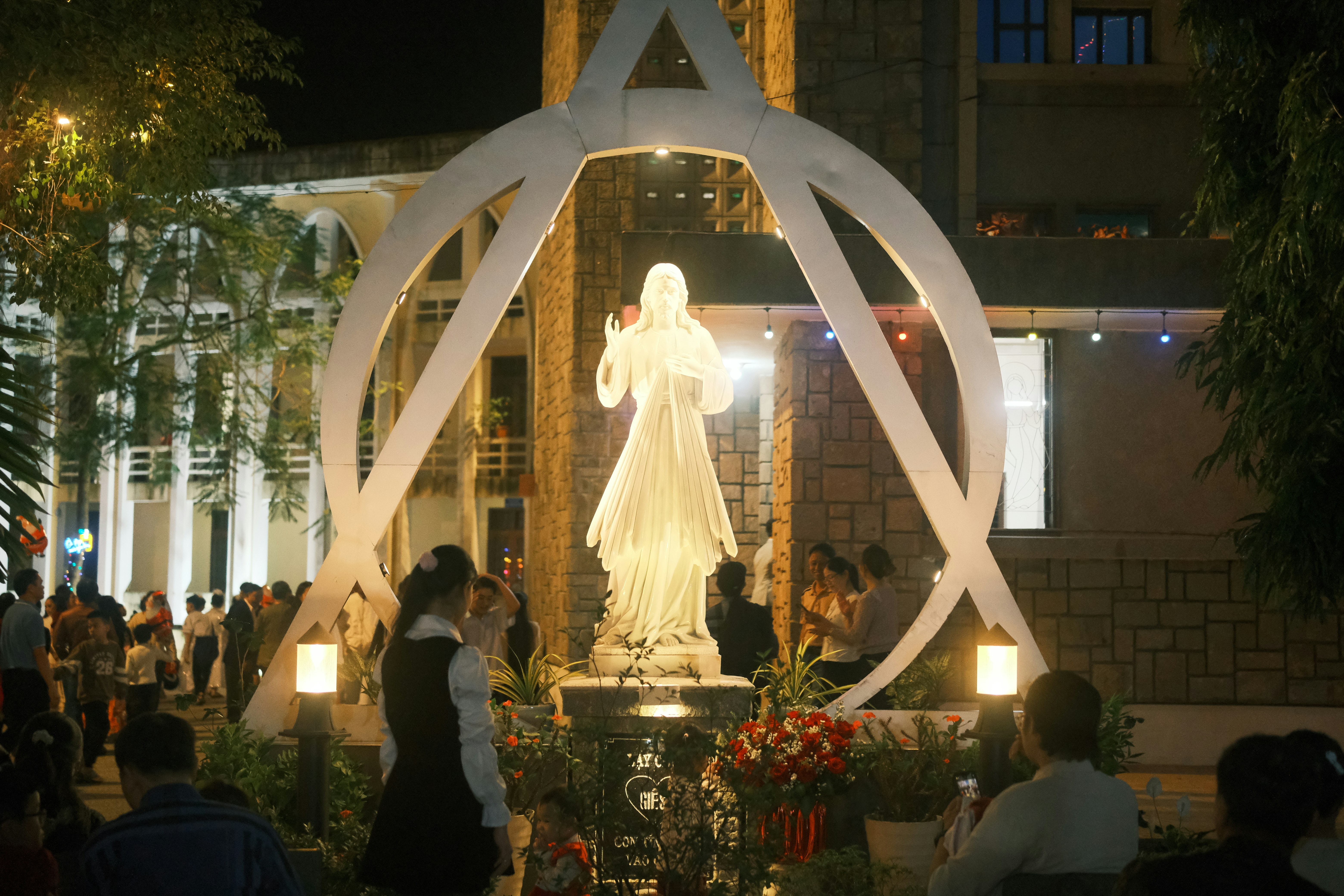 Illuminated statue within a glowing sculpture arch at a nighttime courtyard gathering