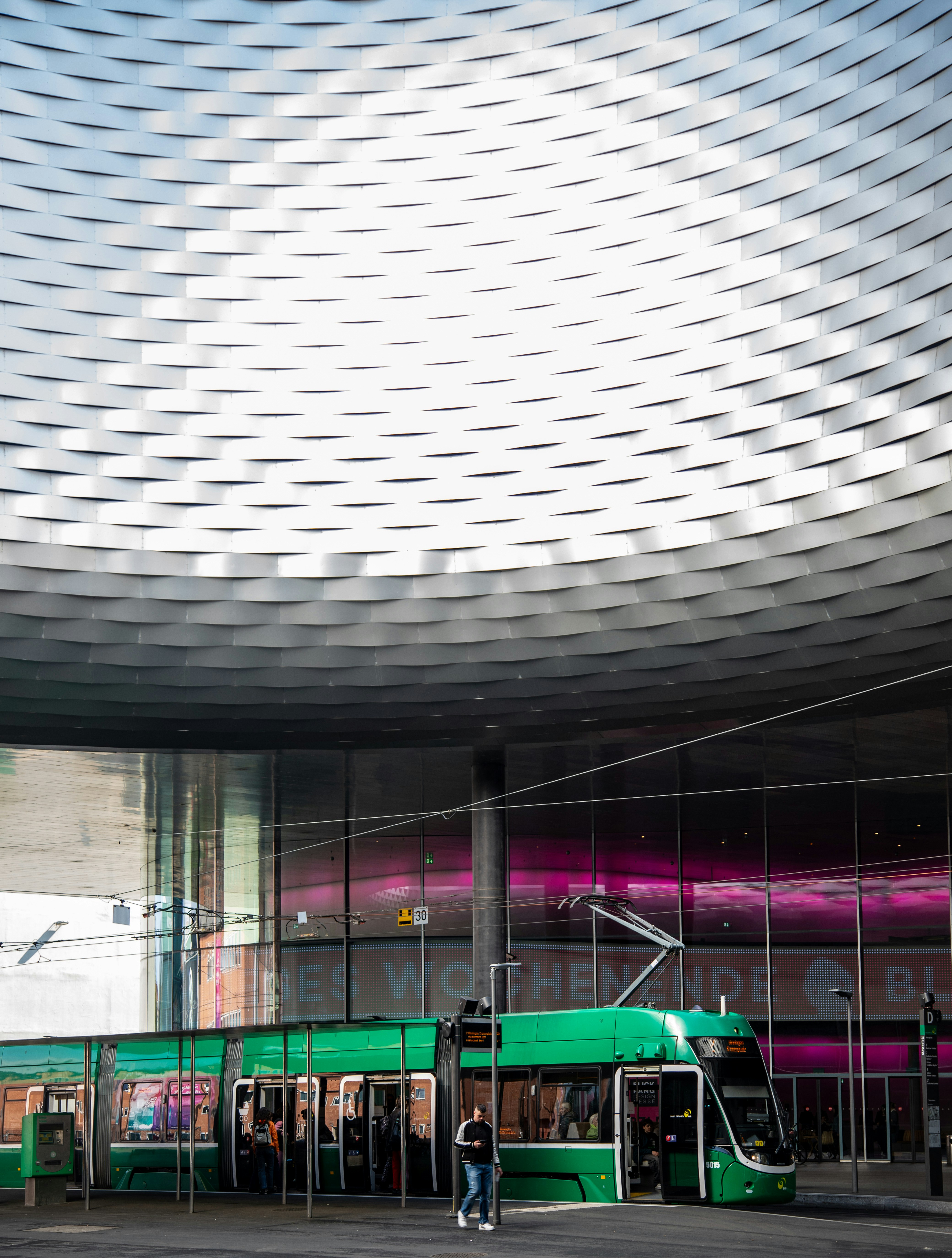 Green tram at the edge of a futuristic plaza under a woven dome