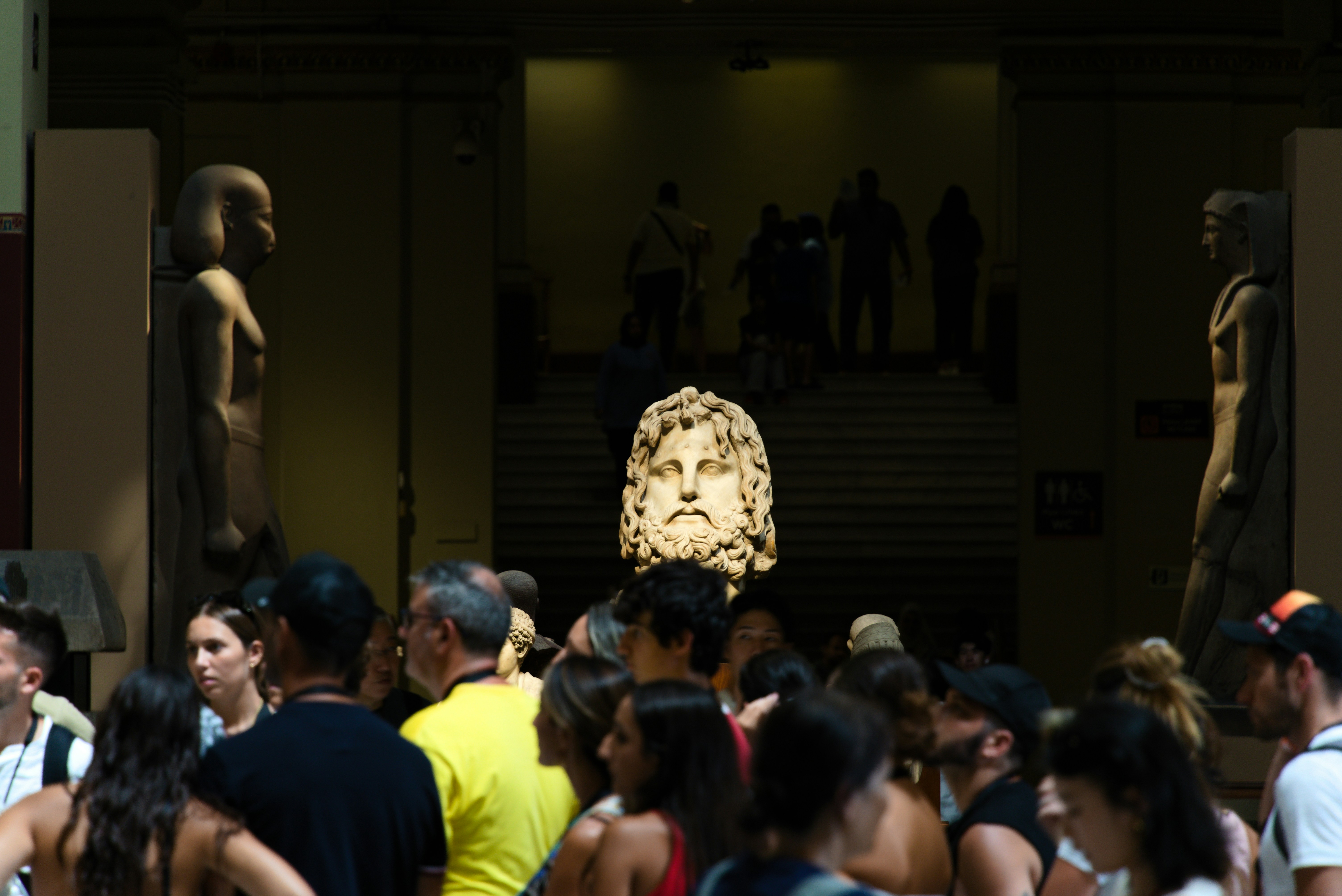 Hero in the Hall: Classical Bust Amid a Modern Gallery Crowd