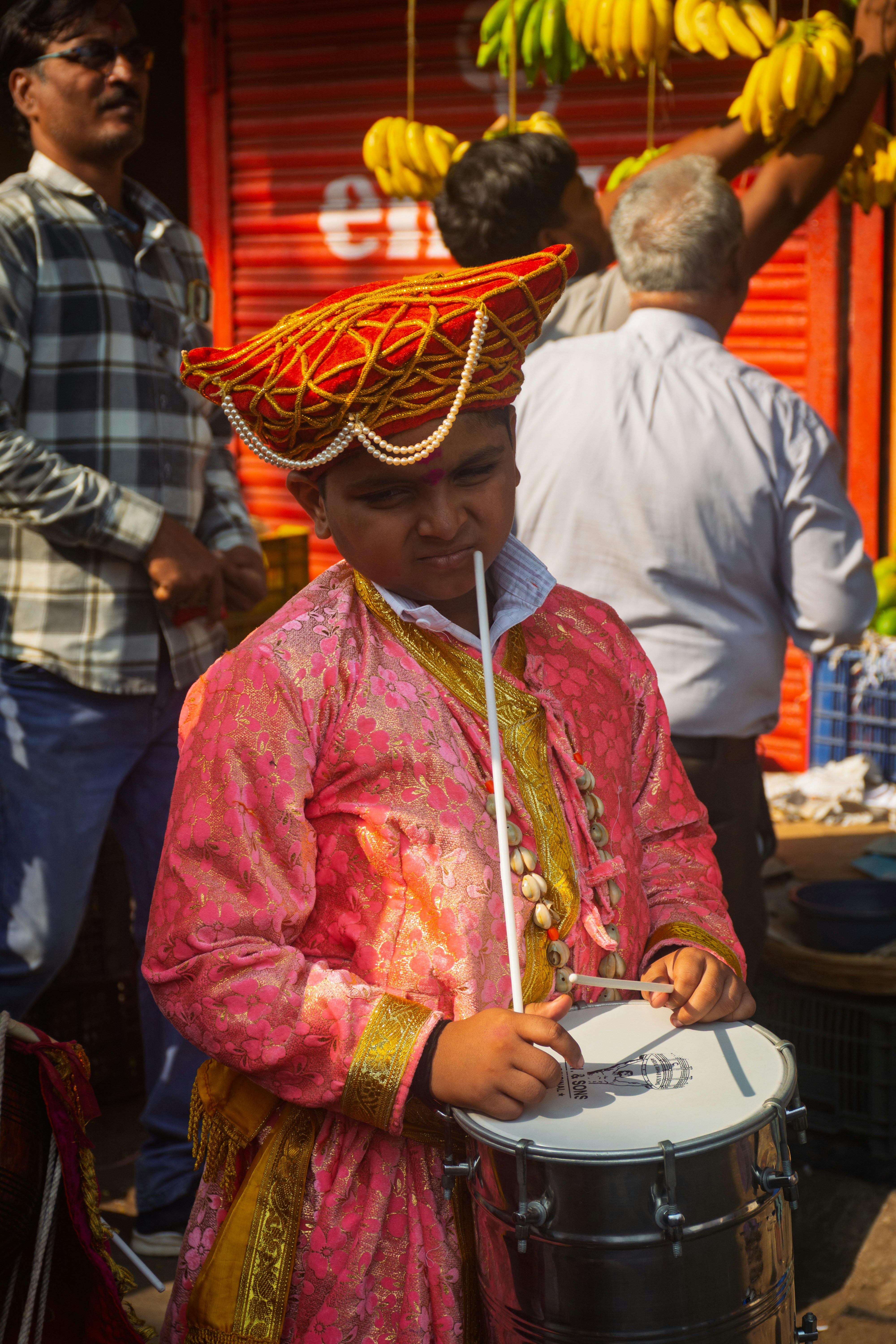 Pink Attire, Drumbeat: A Young Musician in ceremonial dress Plays the Snare under Banana-Lantern Canopy
