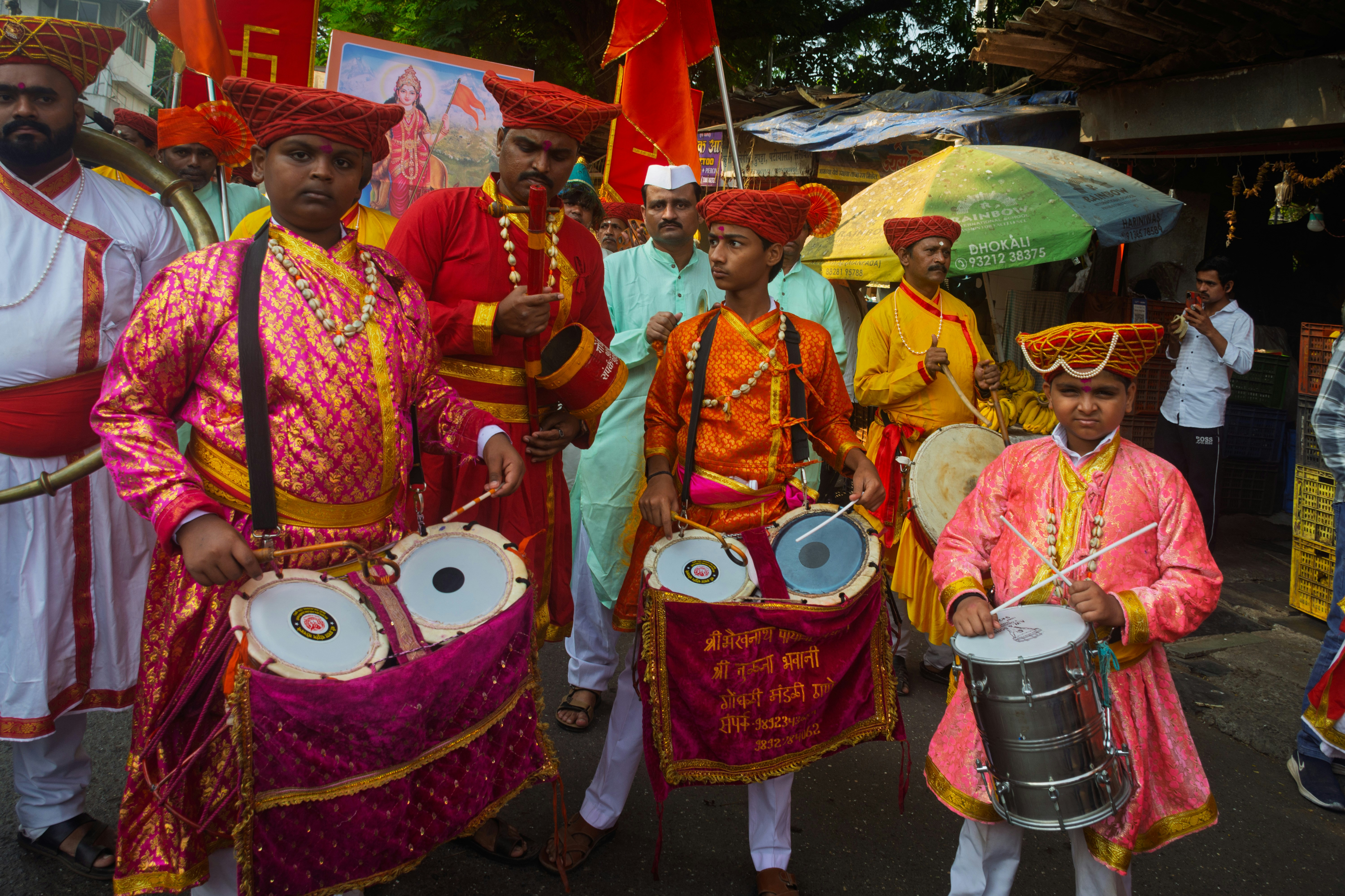 Drummers in vibrant festival attire lead a street procession