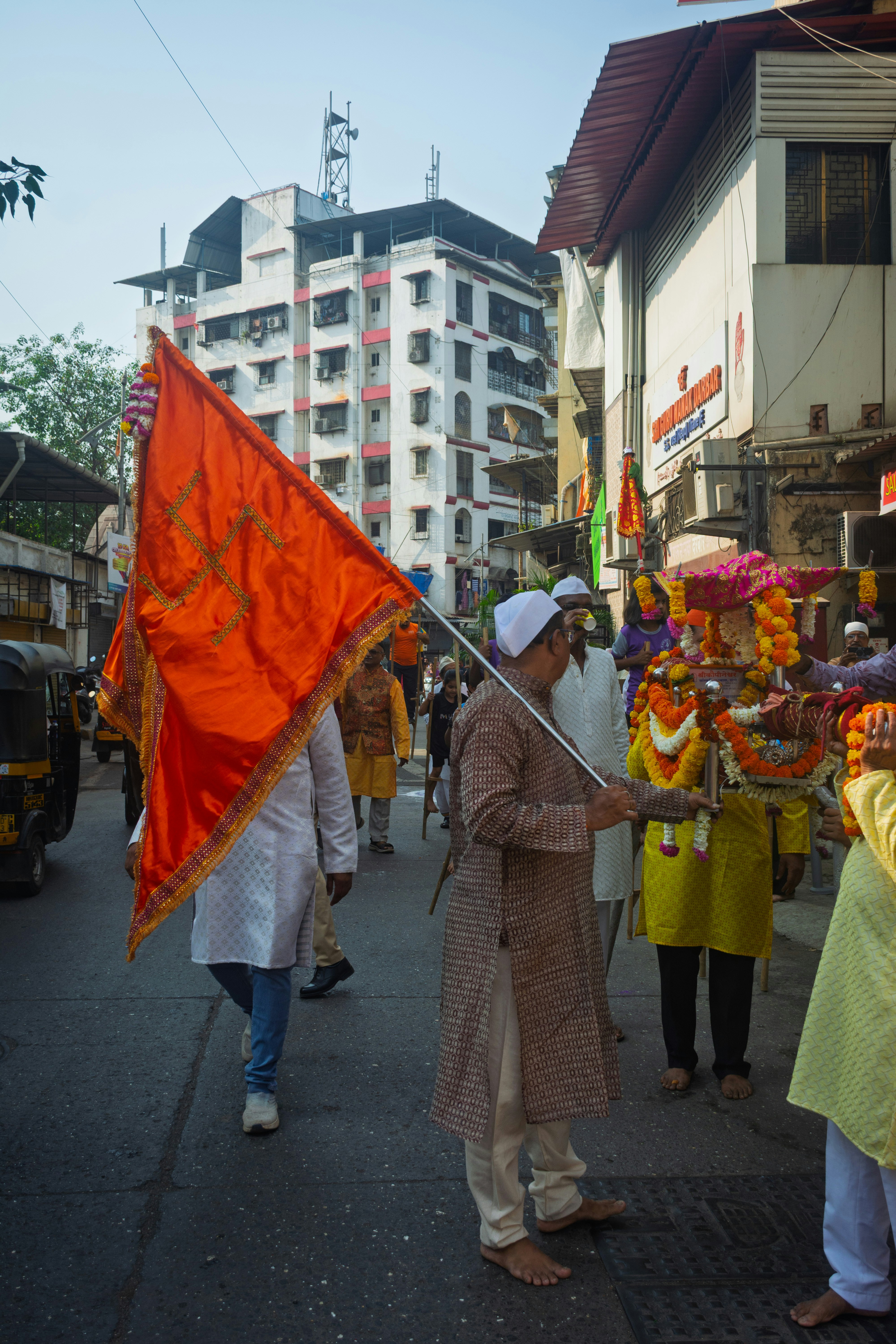 Vibrant street procession: orange banner and garlanded shrine amid a crowded market