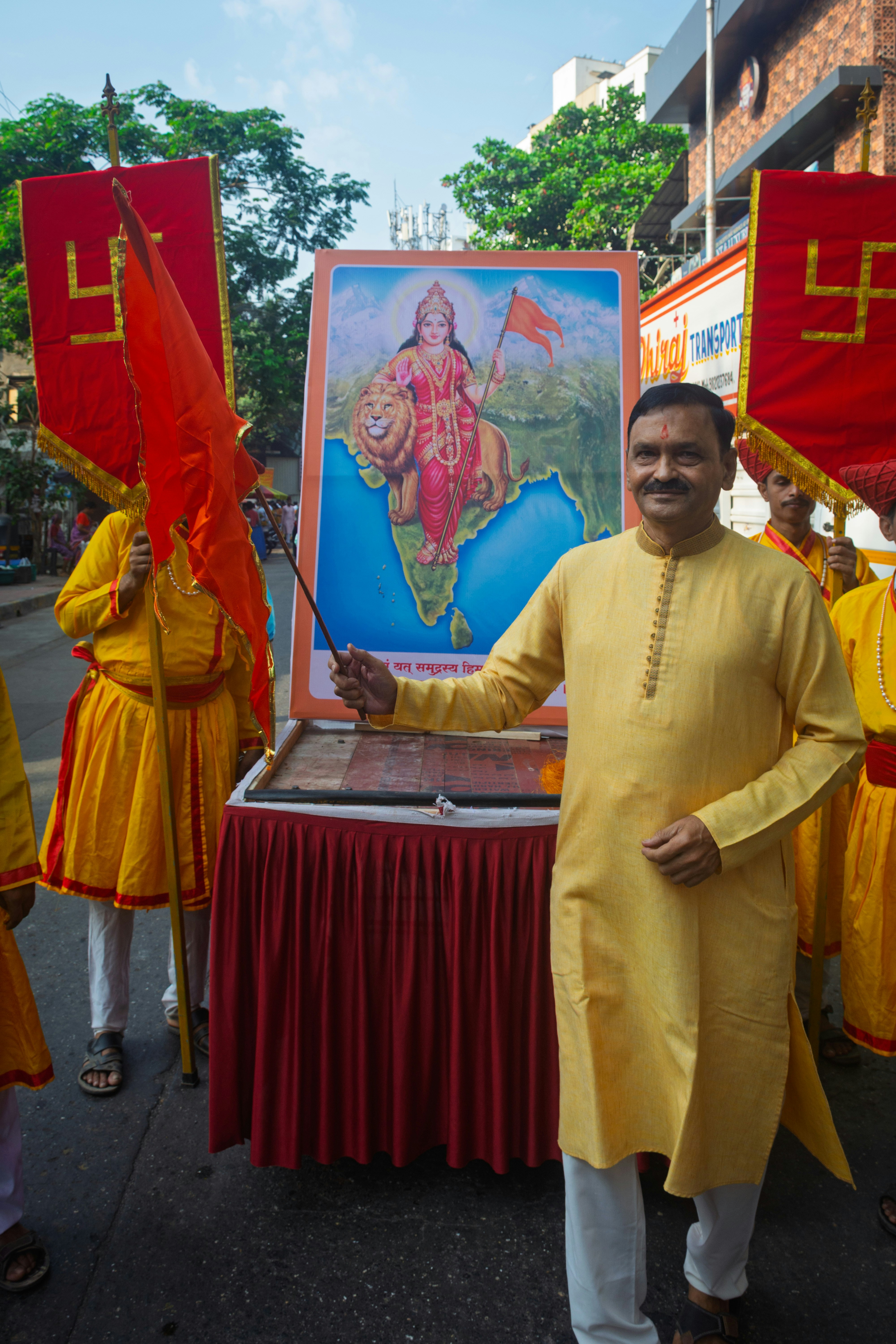Yellow-clad processionist gestures toward a sacred poster during a street display