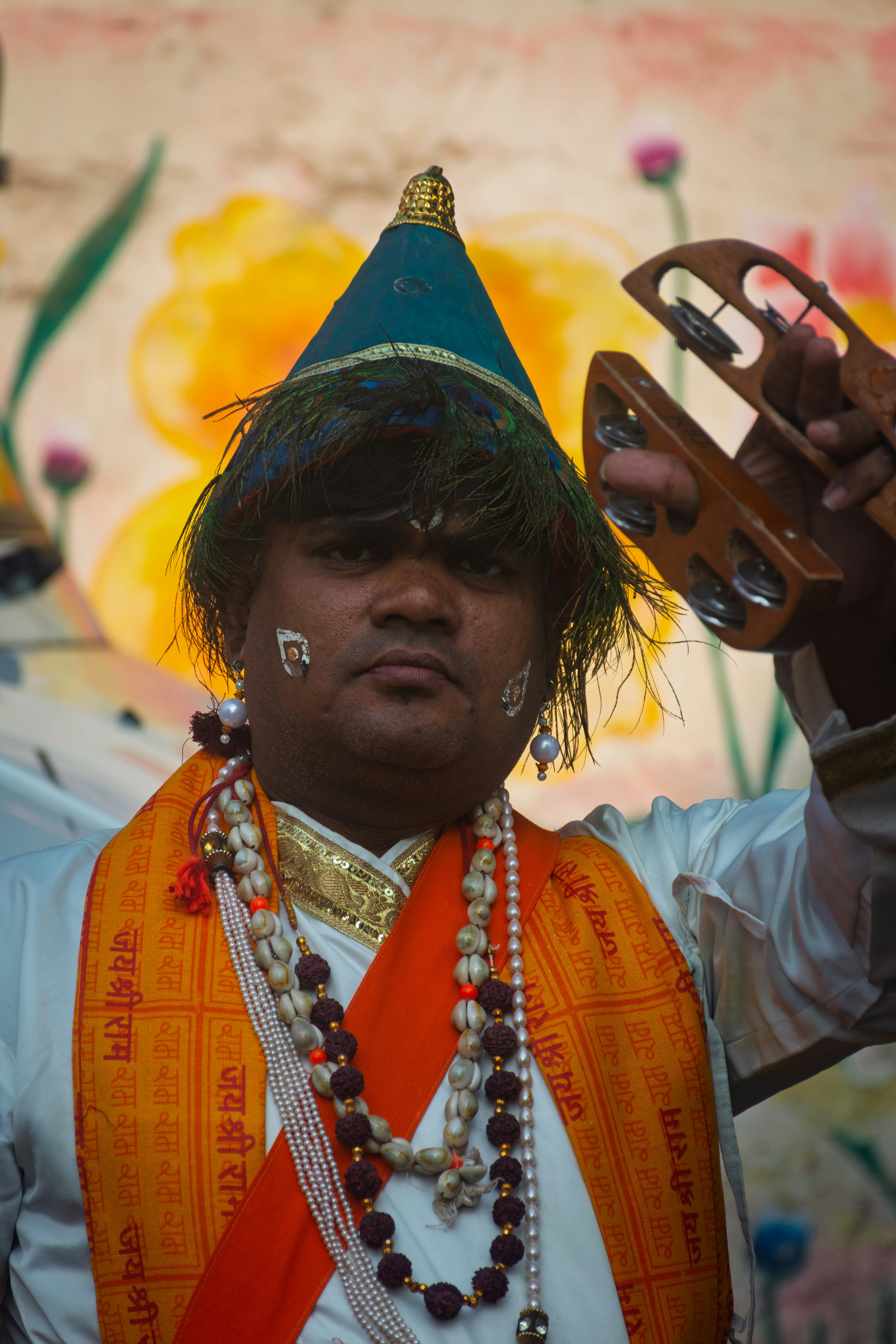 Priest in Orange Sash with Bell Adornments under Blooming Backdrop