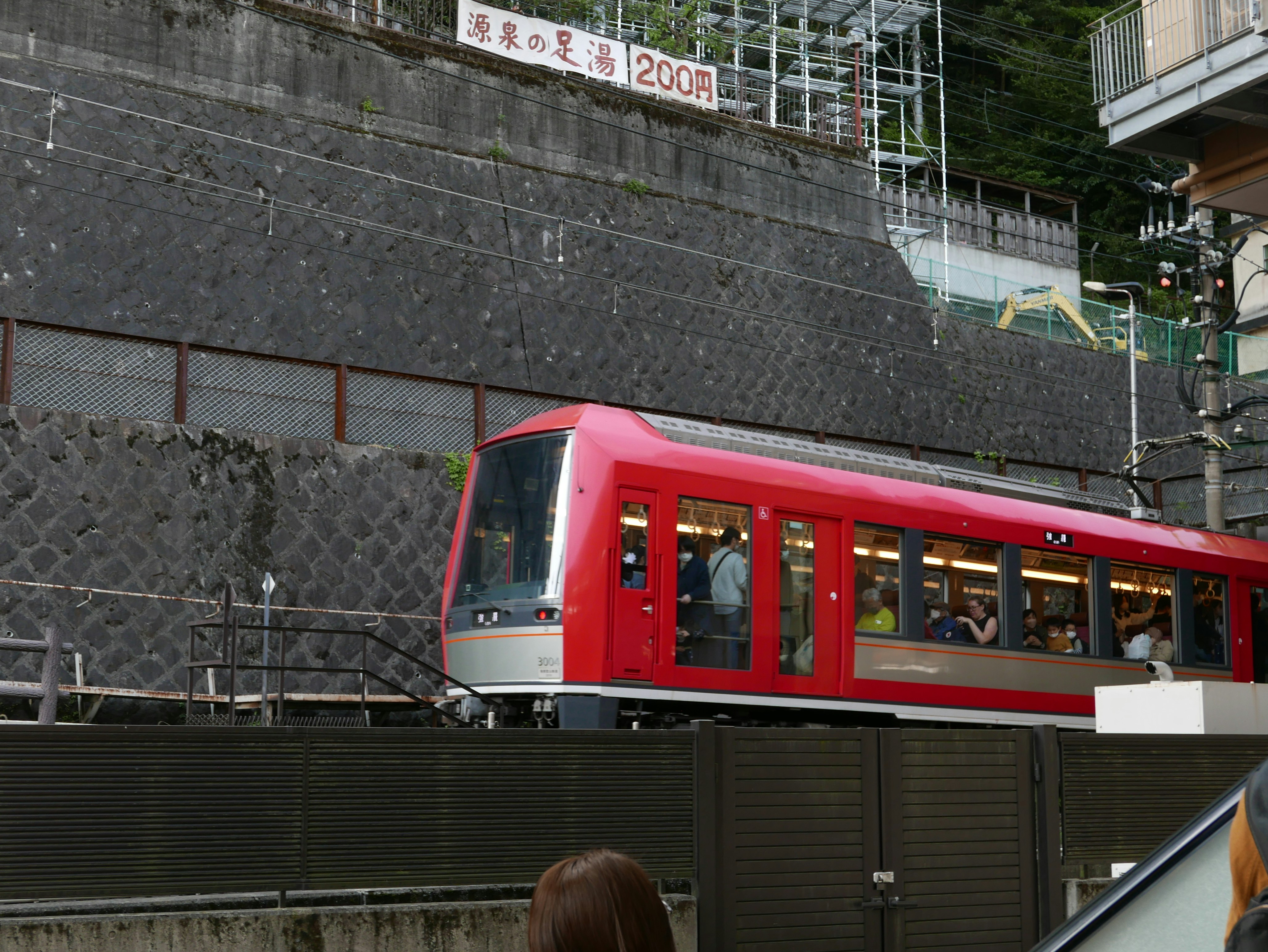 Red commuter car gliding past a concrete embankment