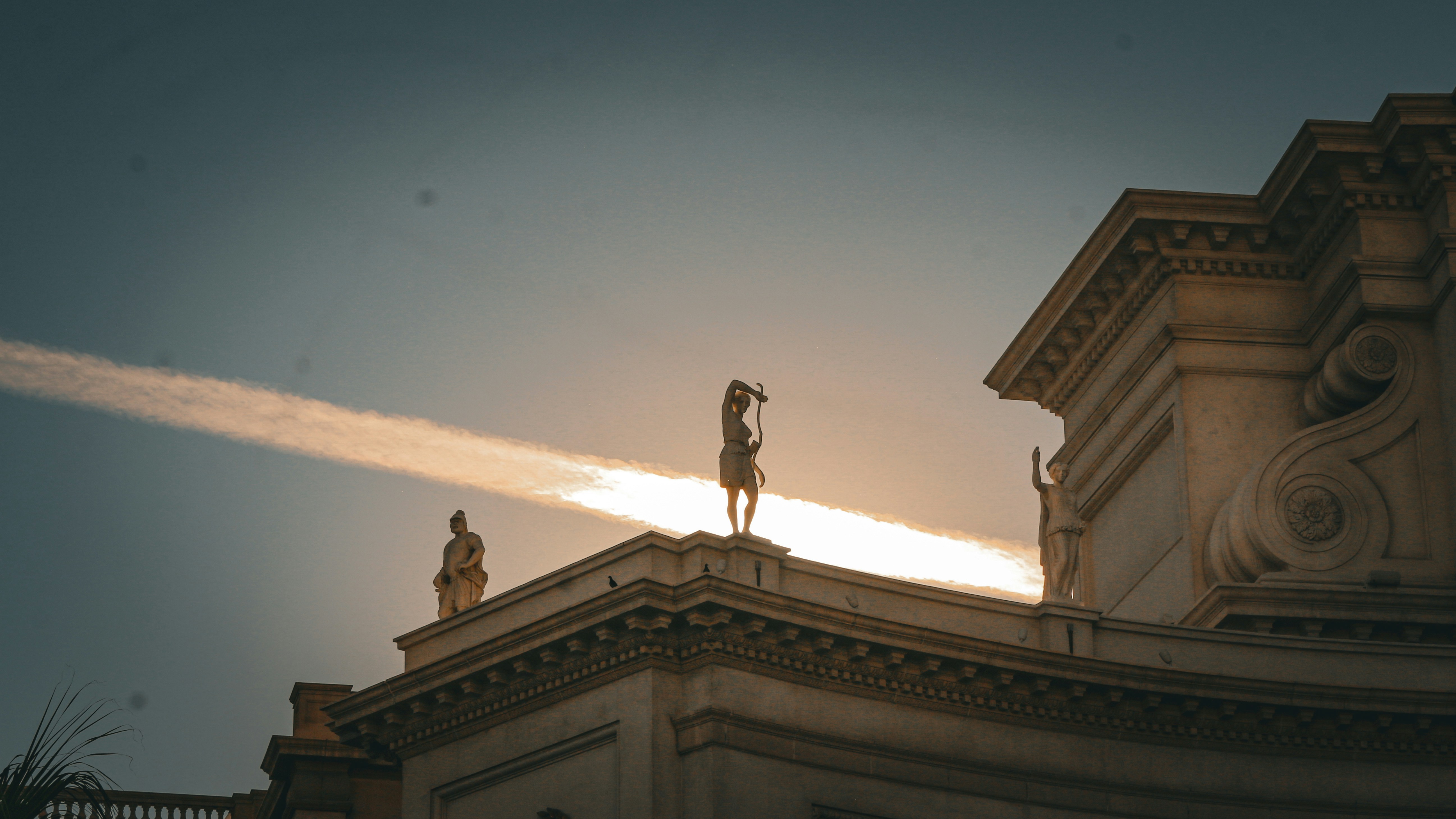 Statue atop a classical roofline catches the last light of day