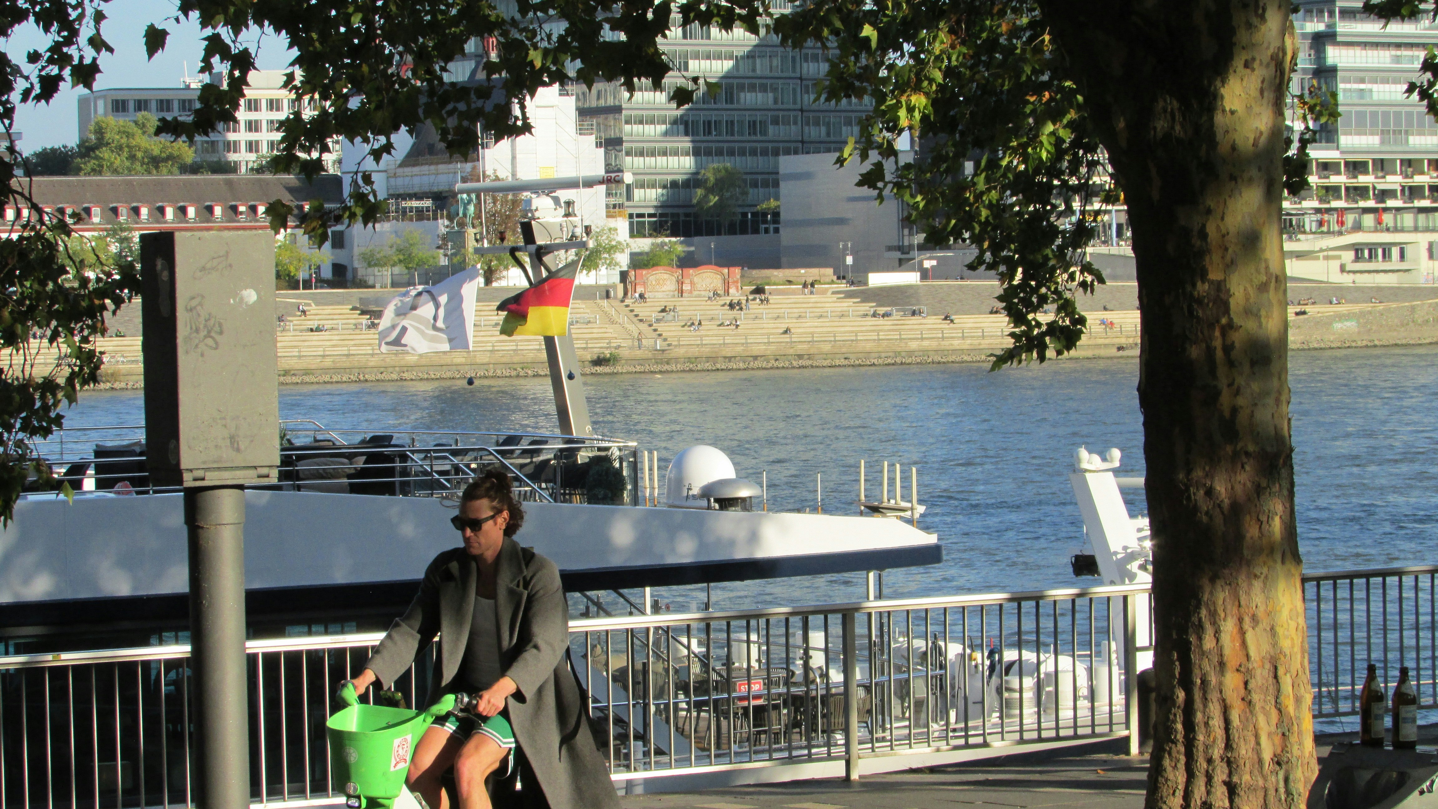 Riverside Rider: A passenger pauses with a bright green basket under leafy framing