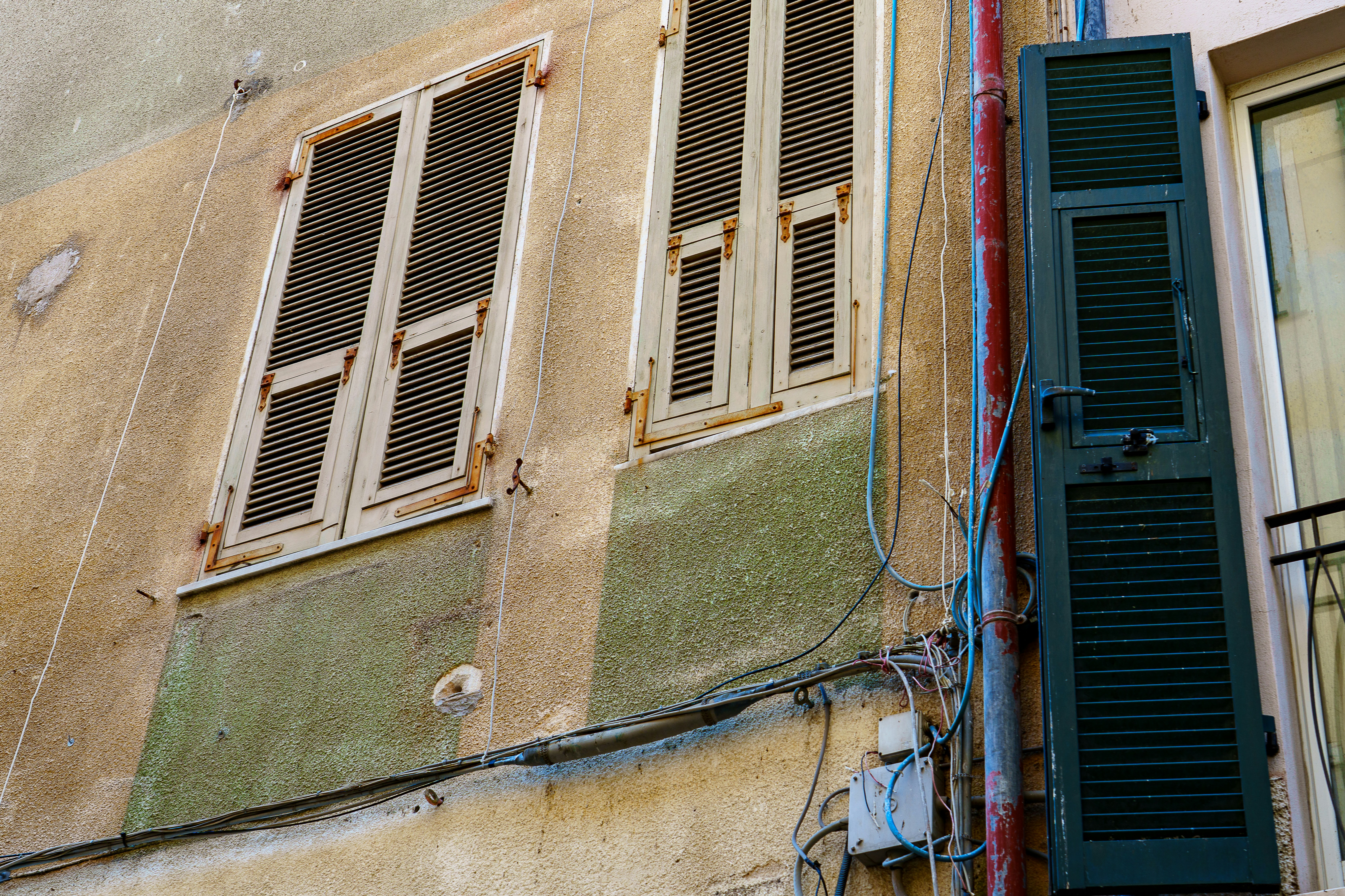 Sunlit Shutters and Wires on a Weathered Facade