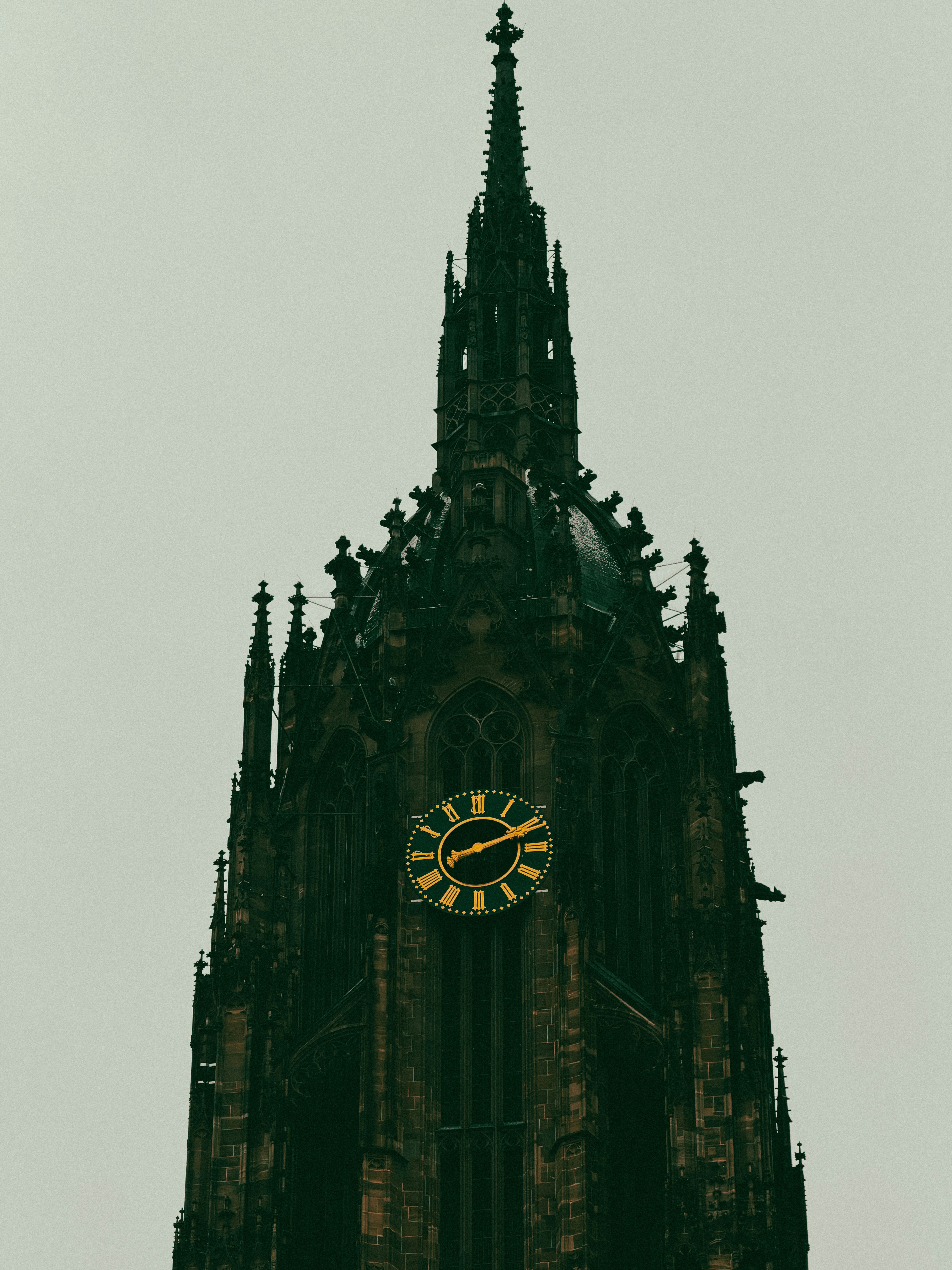 Gothic Spire: Clock and Crowned Peak Against Pale Sky