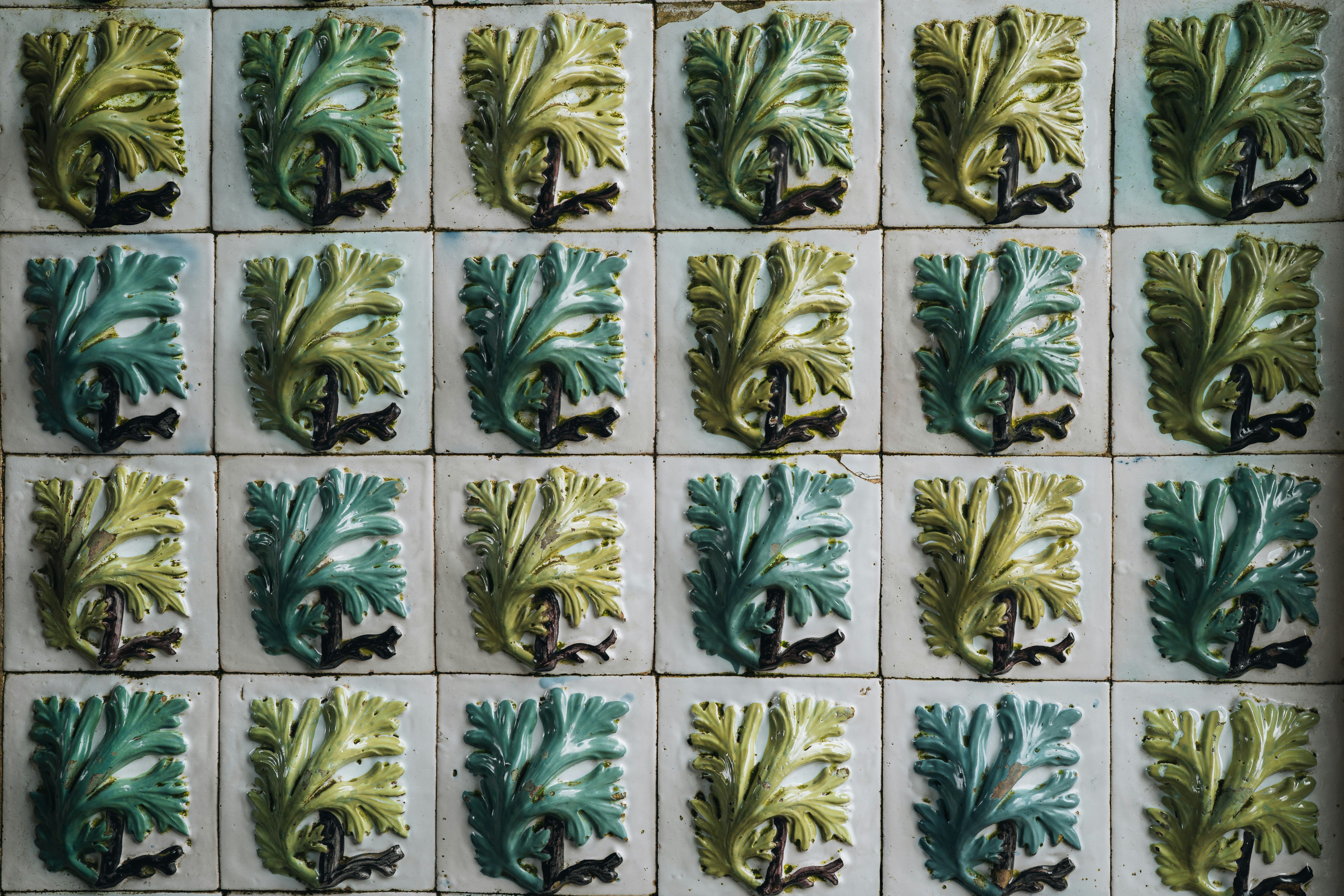 Patterned tile wall featuring stylized plant motifs in alternating green and teal hues arranged in a uniform grid.