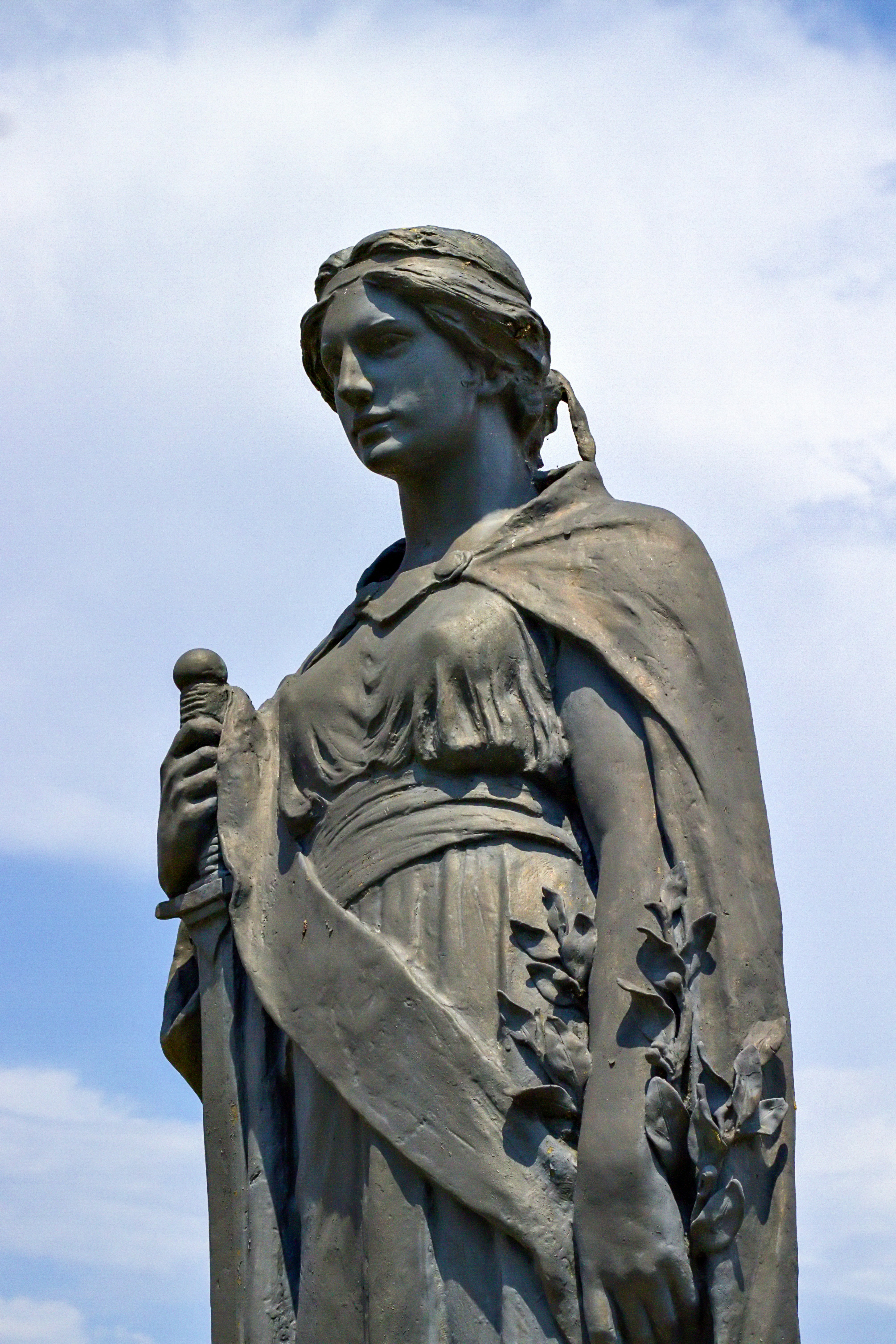 Solemn Sentinel: A Draped Statue Grasping a Sword Against a Sky-blue Backdrop