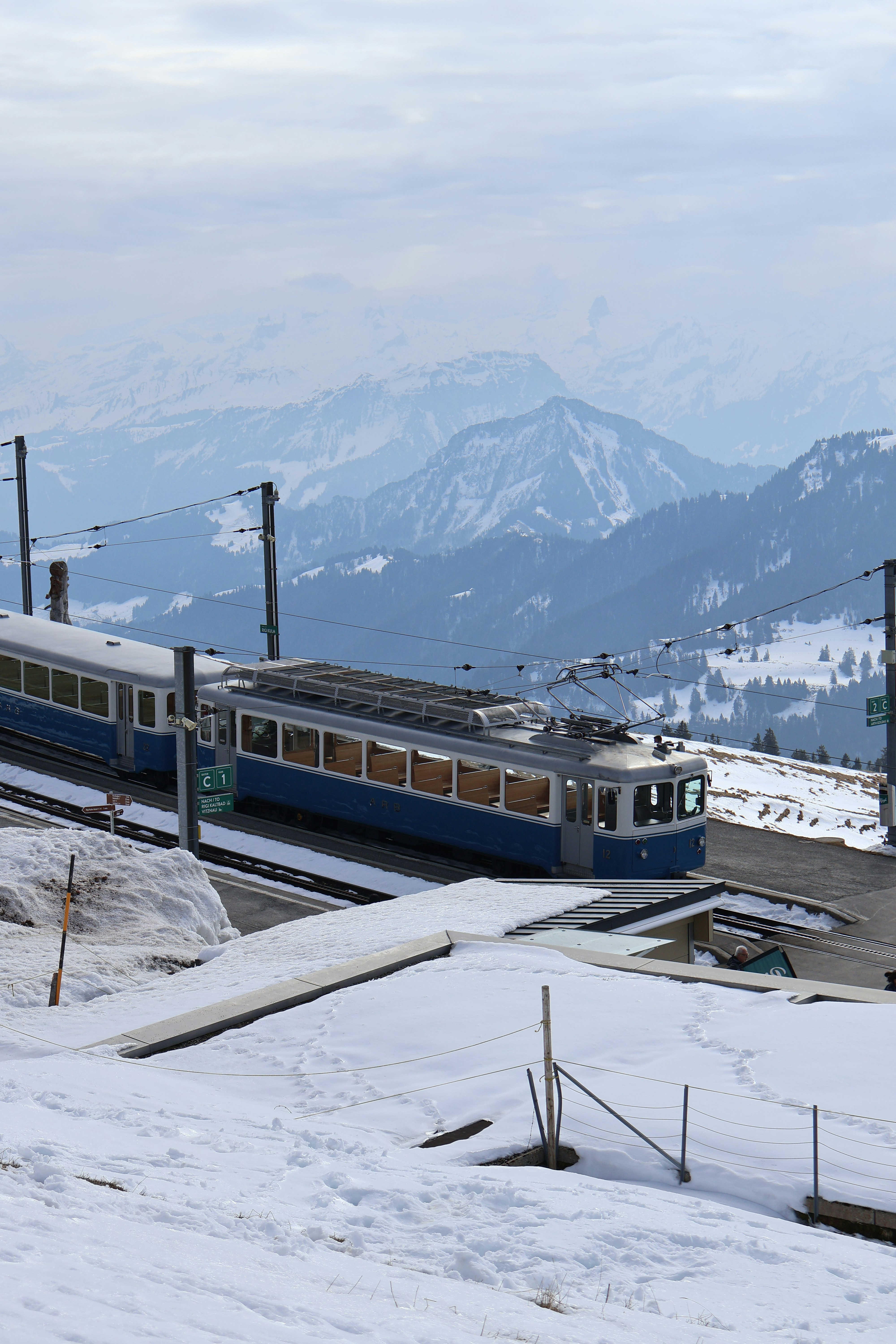 Blue tram carving a snowy hillside toward distant Alps