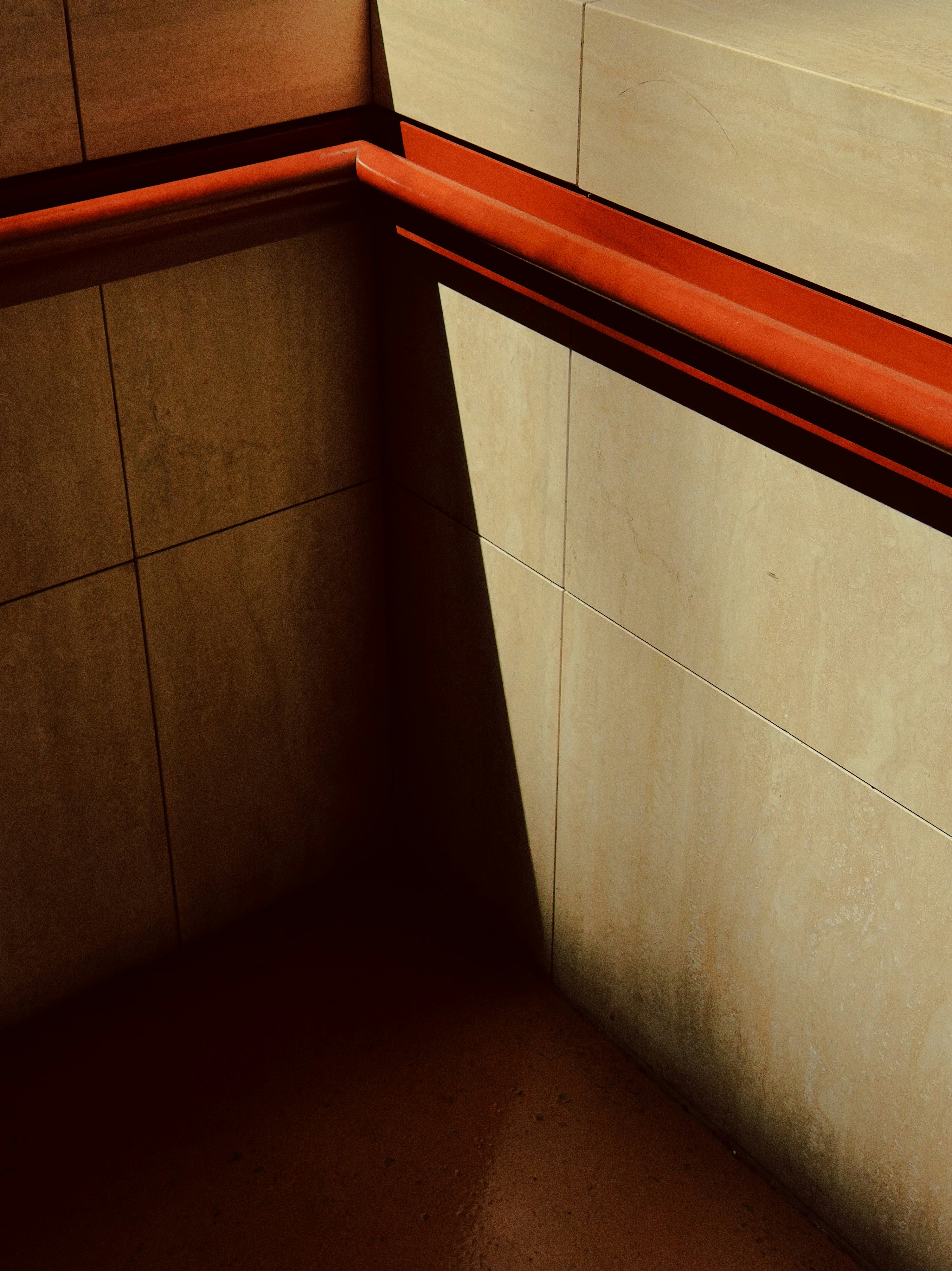 Shadowed Corner: Red Railing Hugs Beige Tile