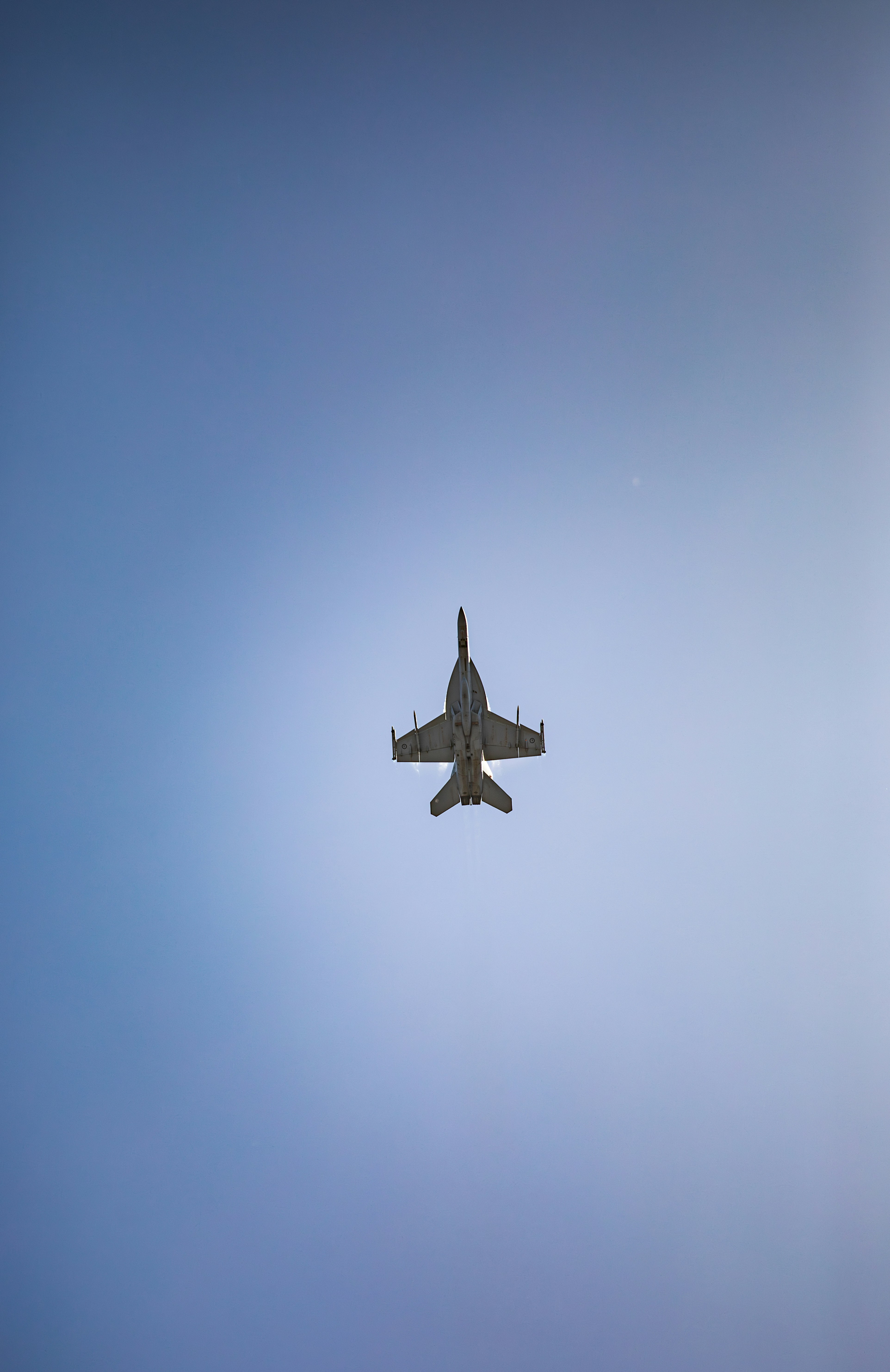 Midair silhouette: a lone aircraft climbs through a pale blue sky