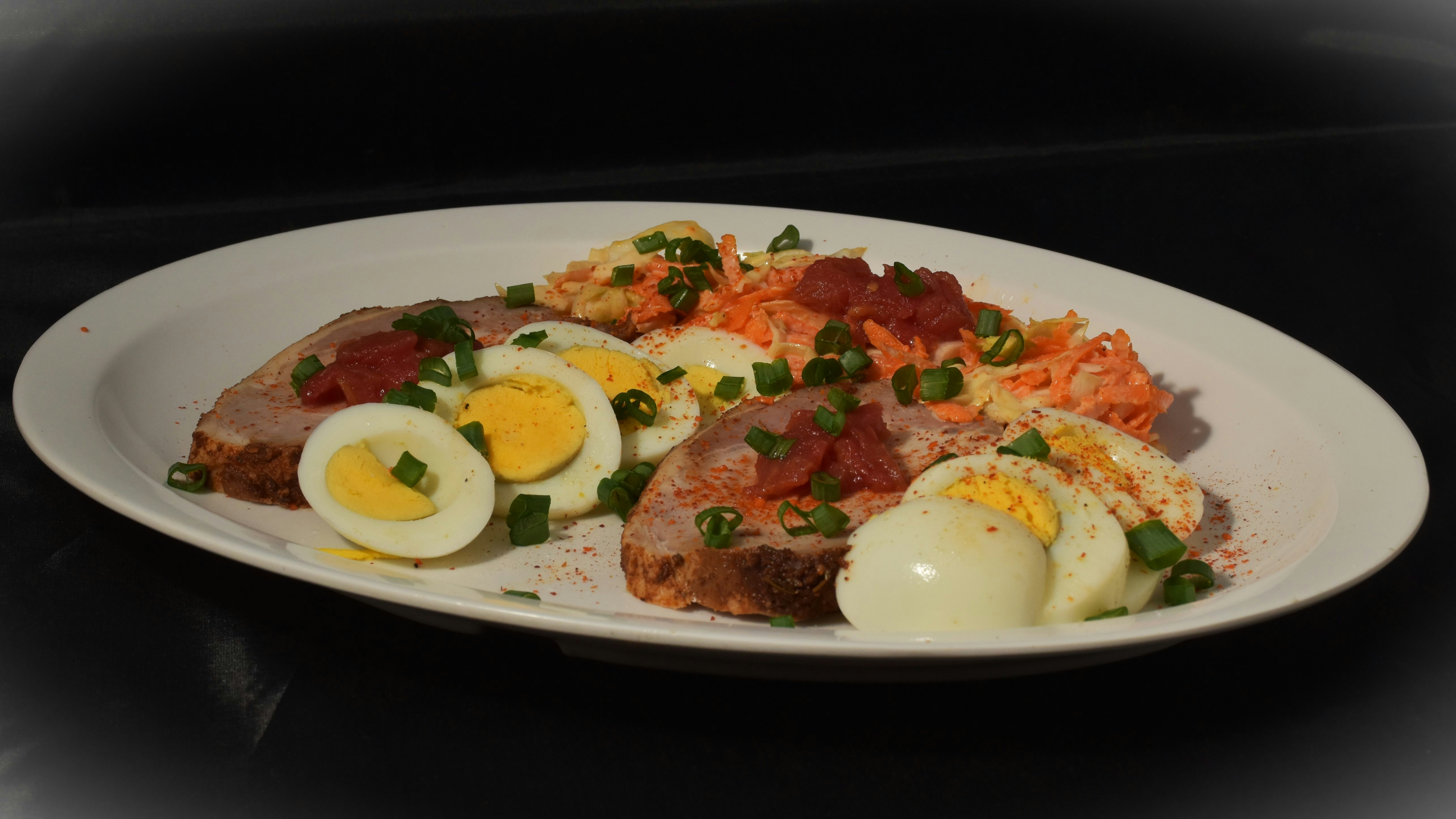Plate of sliced beef with hard-boiled eggs and greens on a white dish