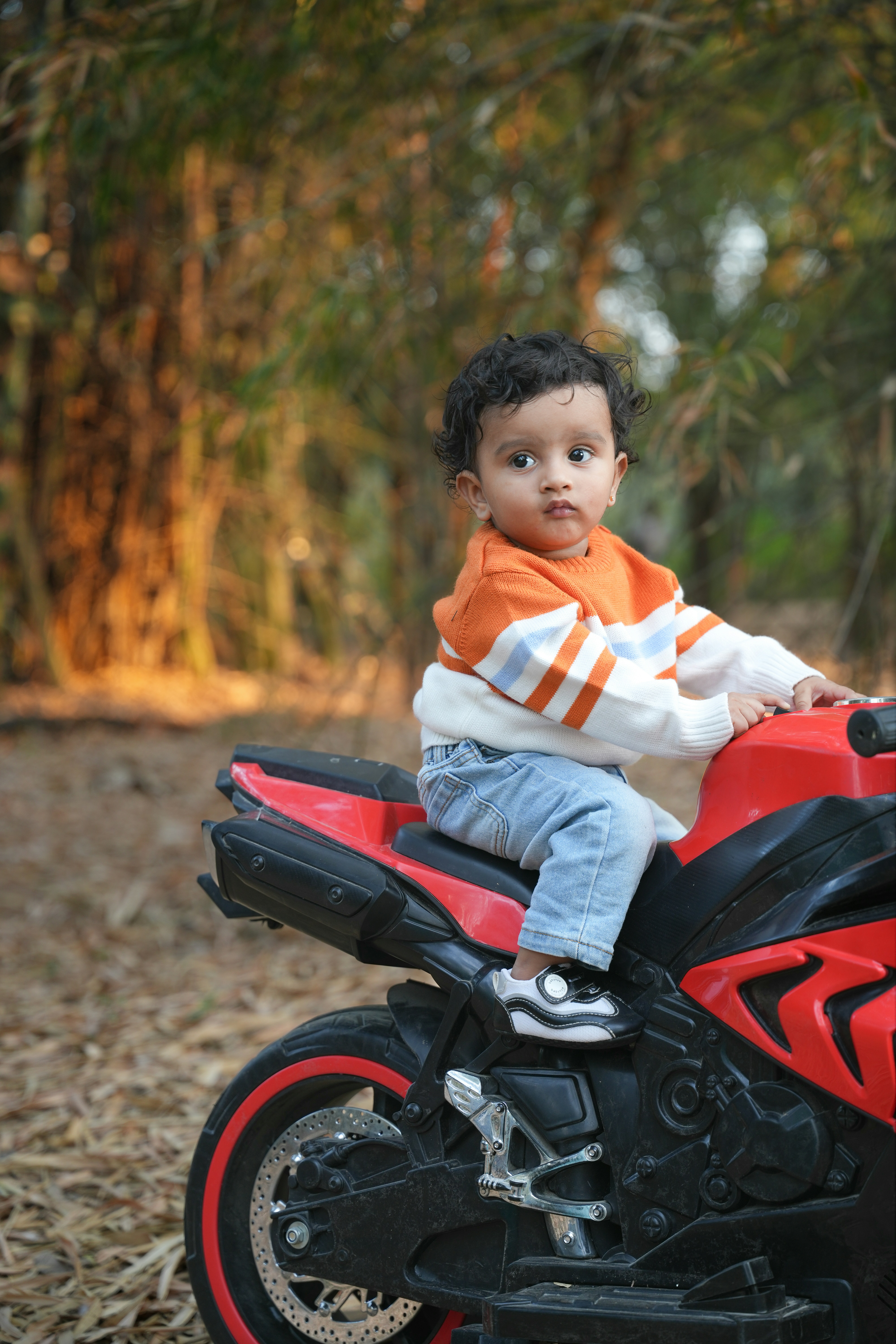 Child on a red sport motorcycle in a sunlit forest clearing