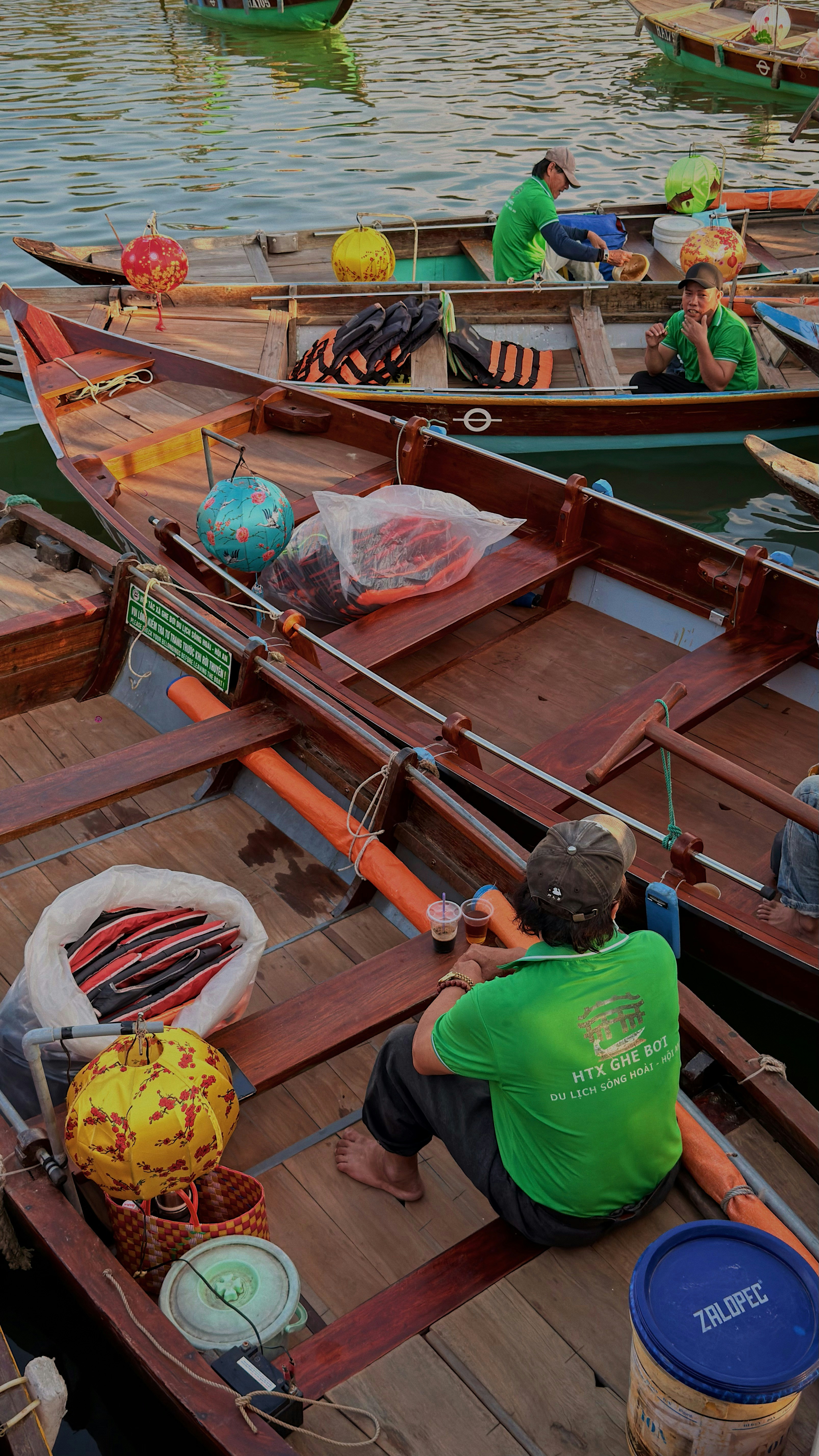 Green-shirted boat hand amidst a harbor of wooden vessels