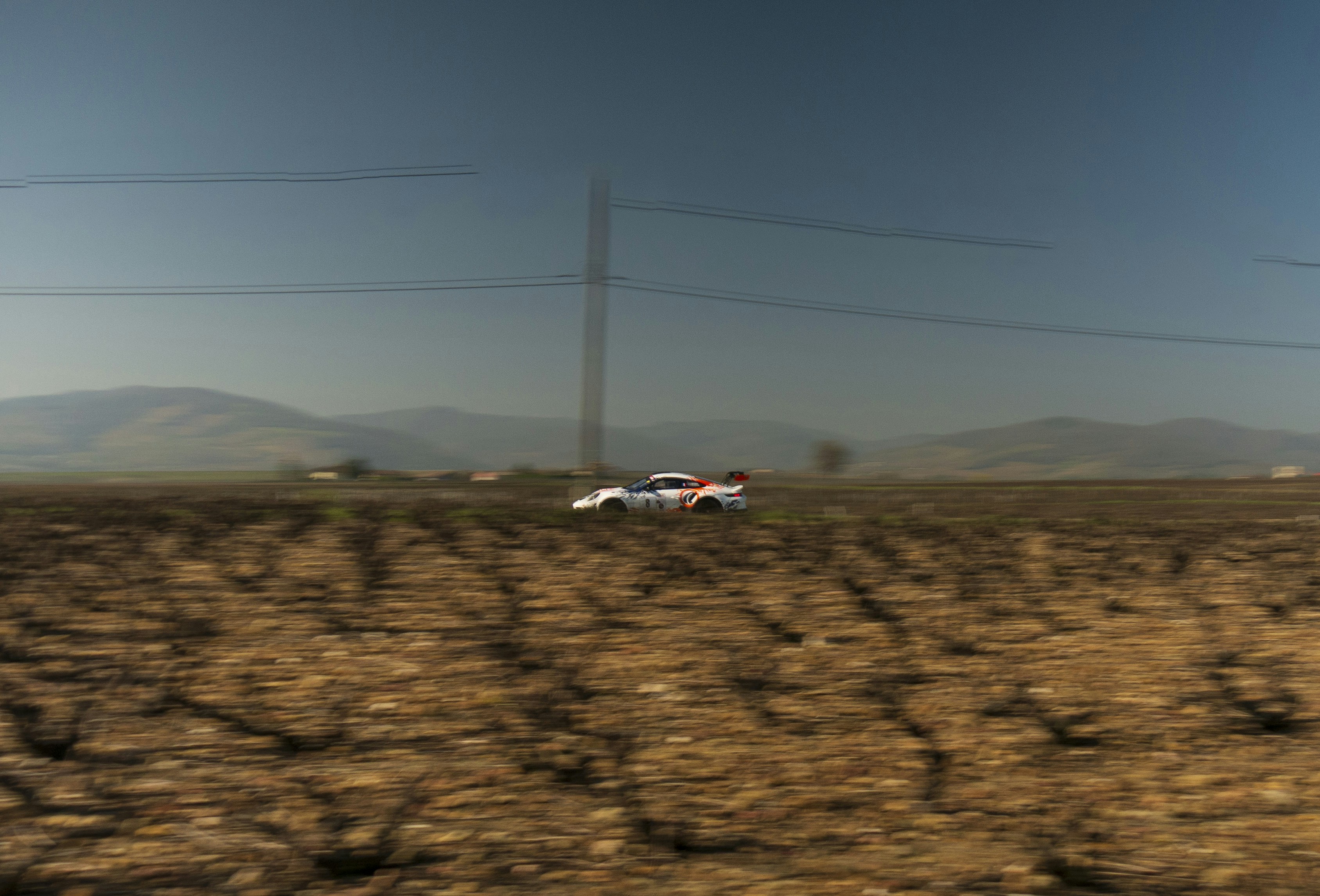 Racing Silhouette: A Distant White Car Speeds Across a Desert Plain