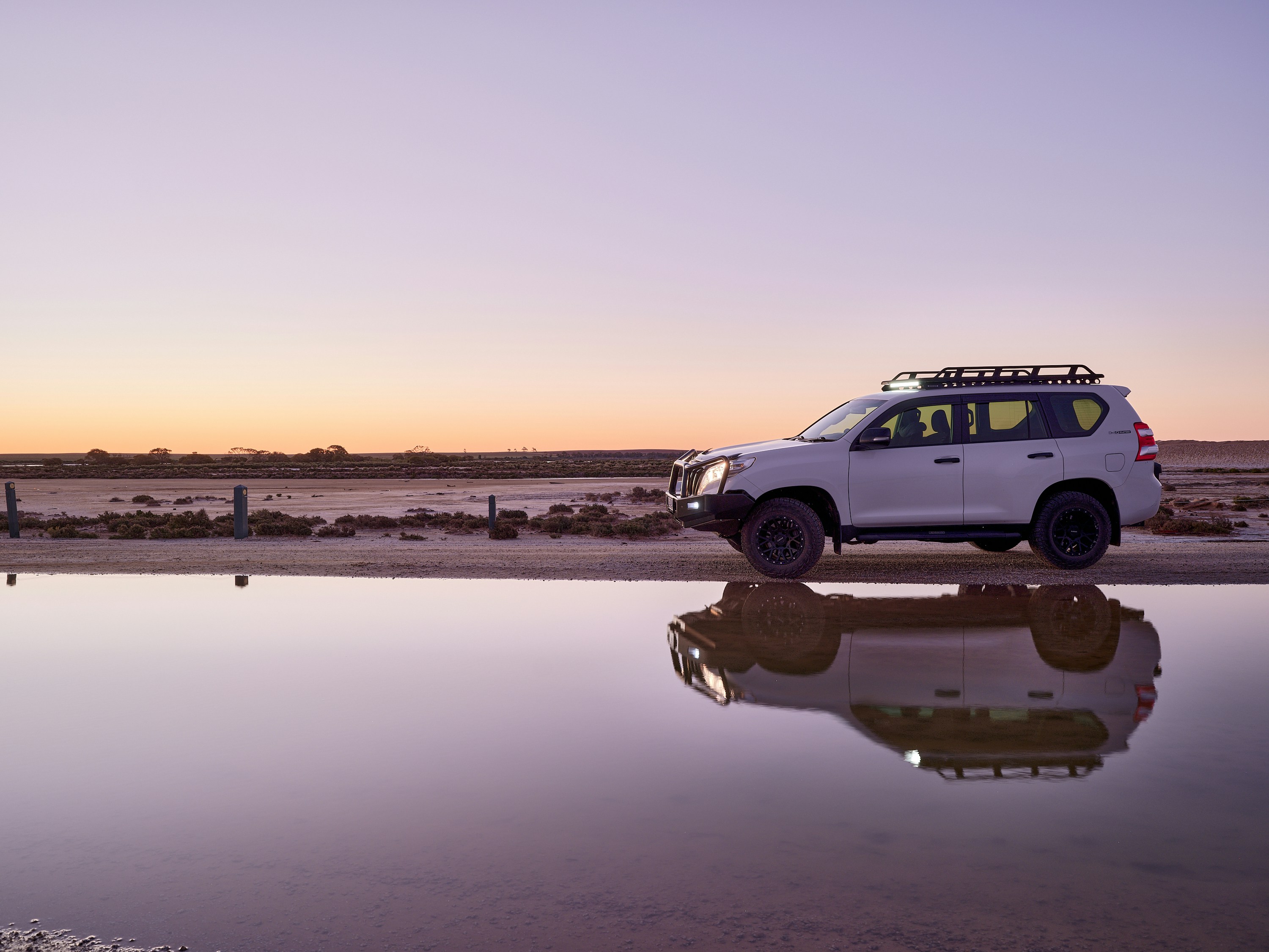 Ridge Horizon: A white SUV on a mirrored desert pool at sunset