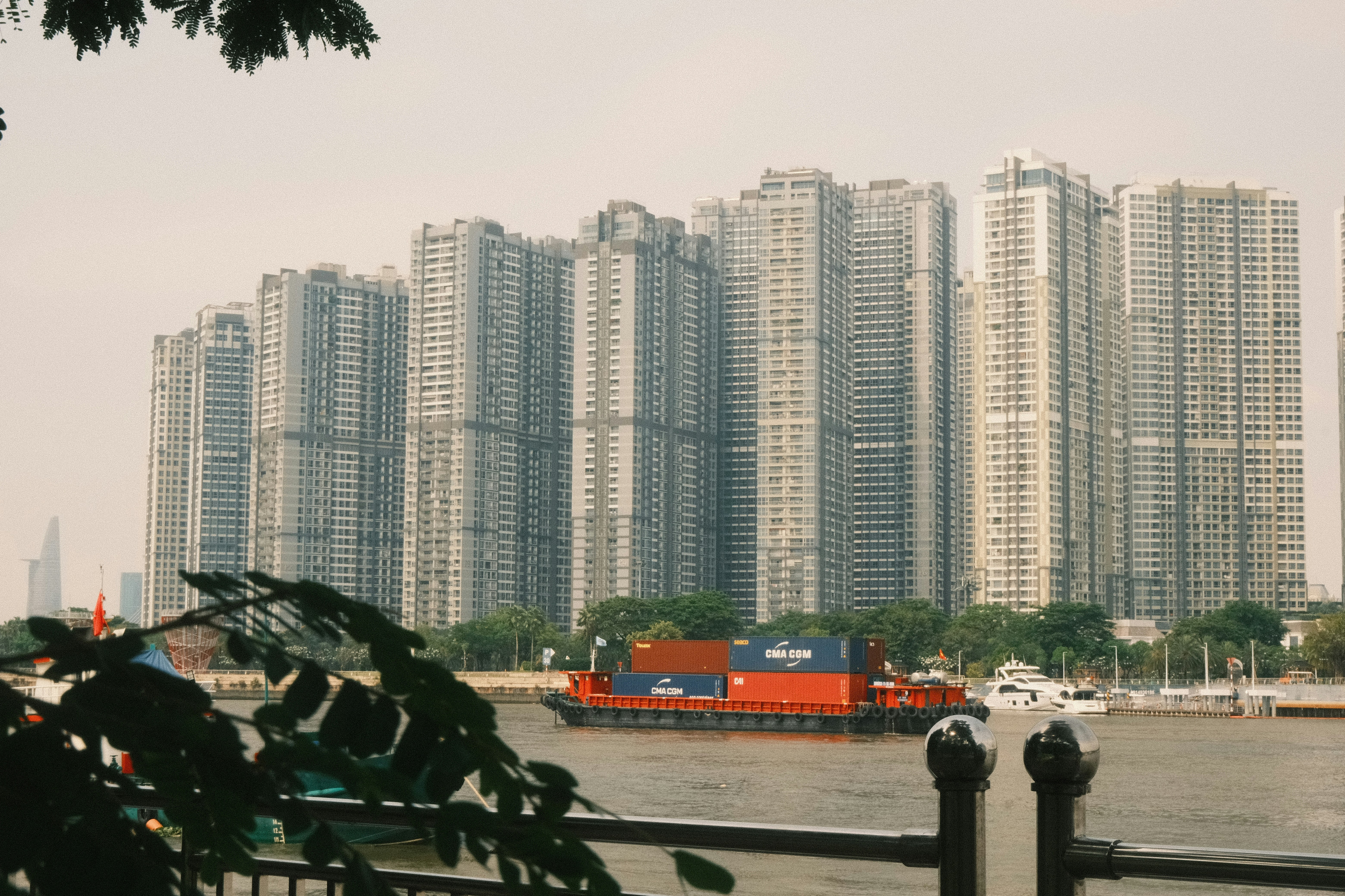 Red and white cargo barge gliding past a skyline of modern towers