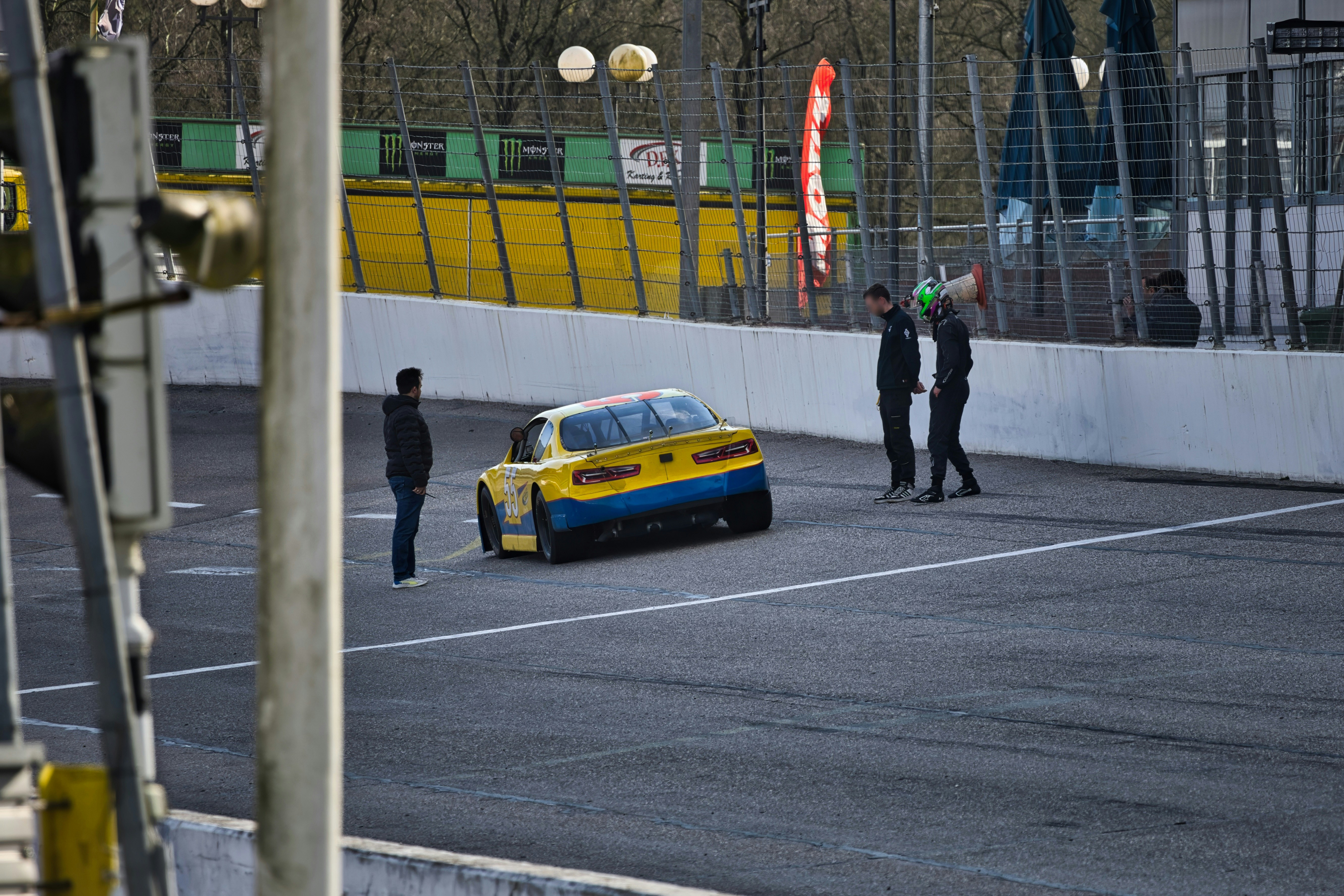Yellow race car at pit lane with crew and barriers