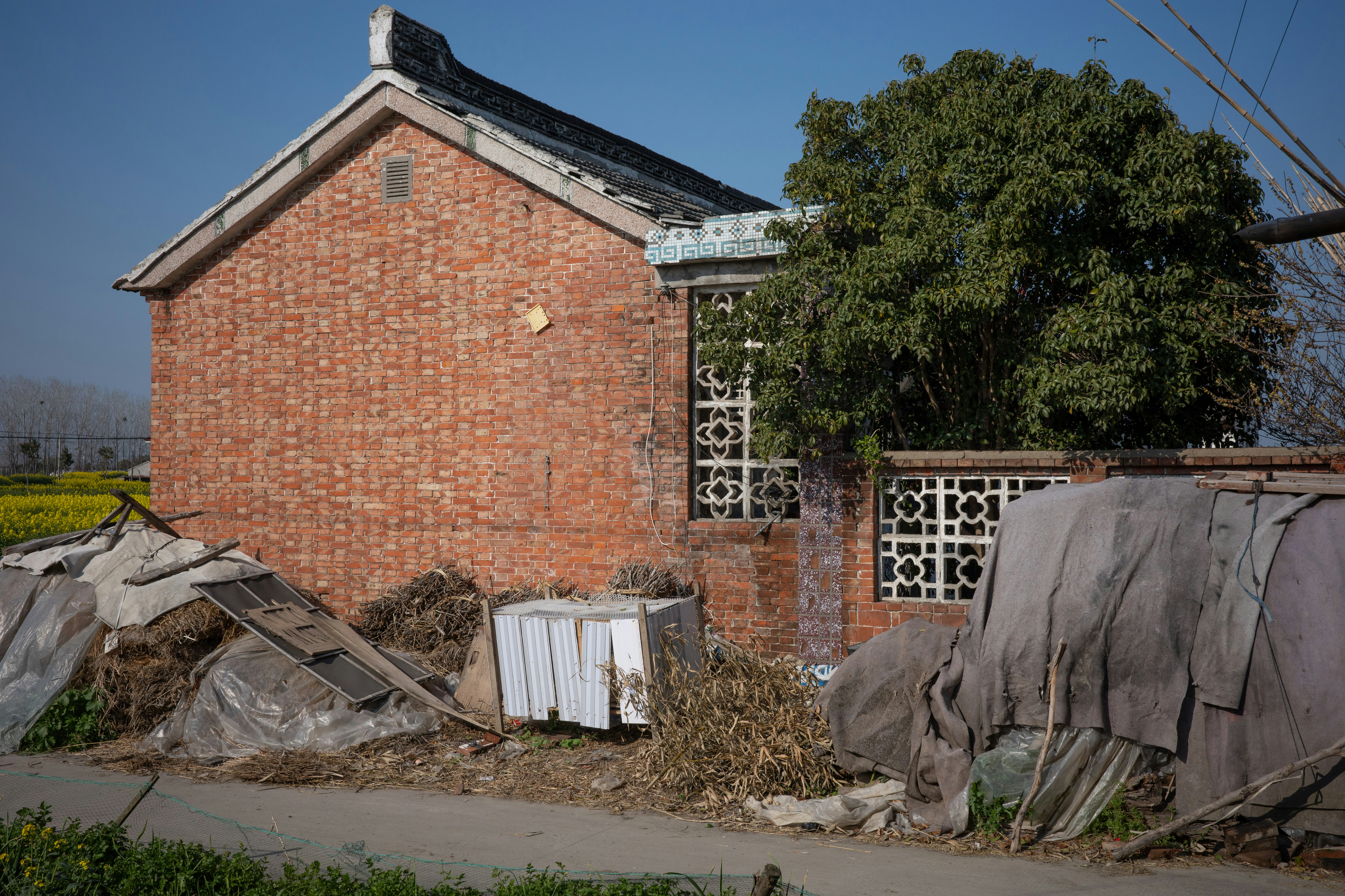 Abandoned brick cottage with cluttered foreground under a clear sky