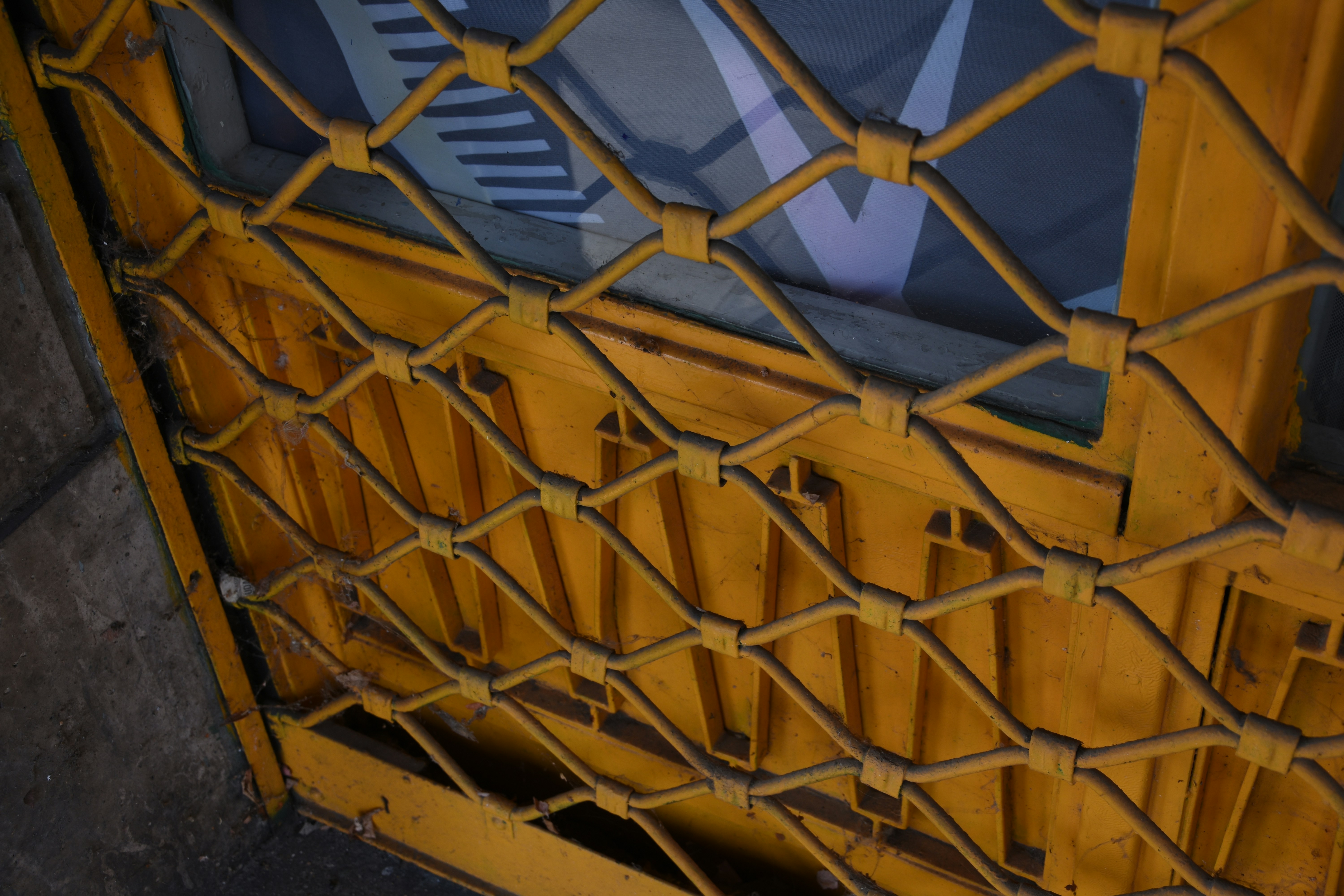 Gridwork of Rust and Rigging: A Woven Barrier in Urban Yellow
