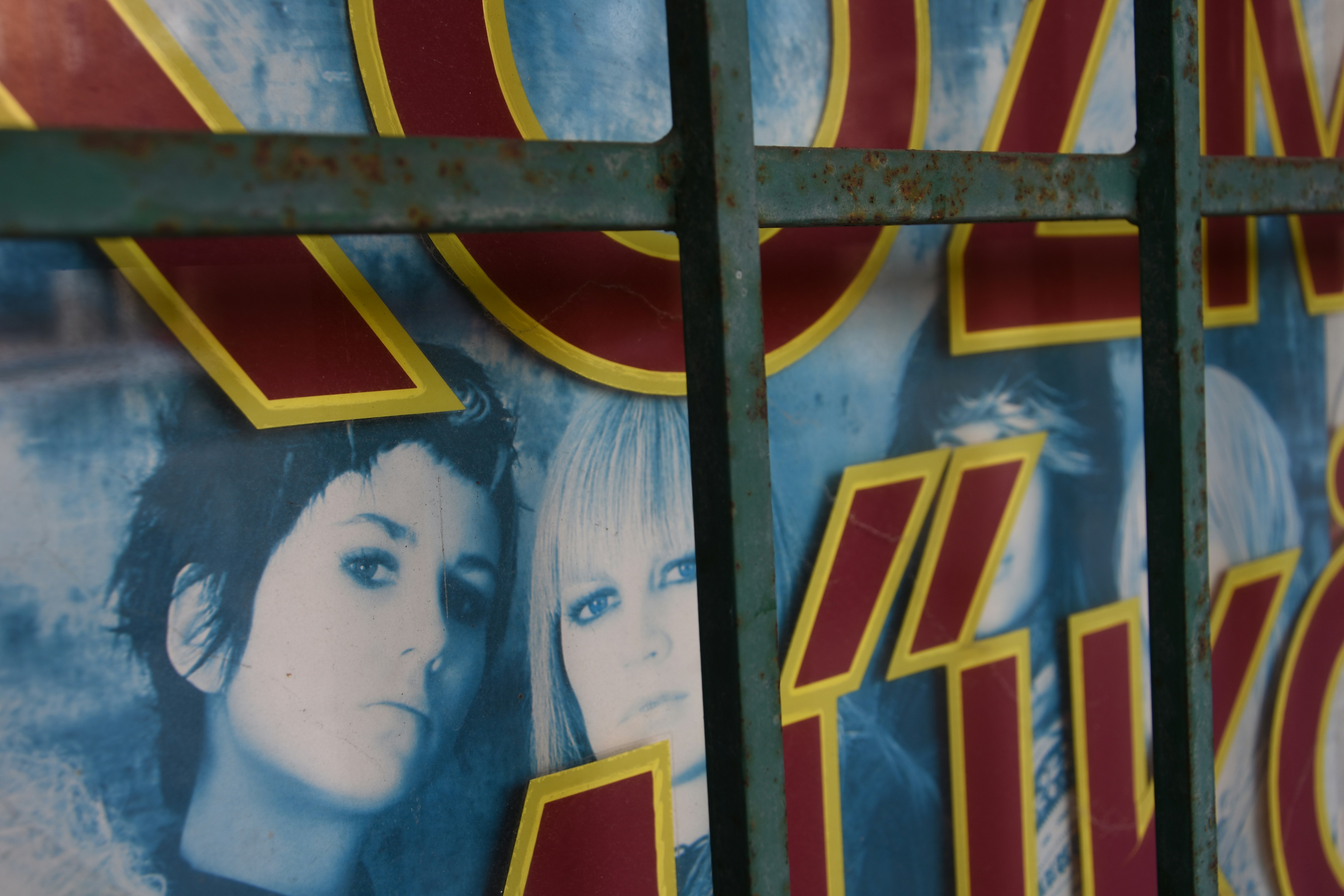 Framed by Rust and Neon: Faces Behind a Weathered Sign