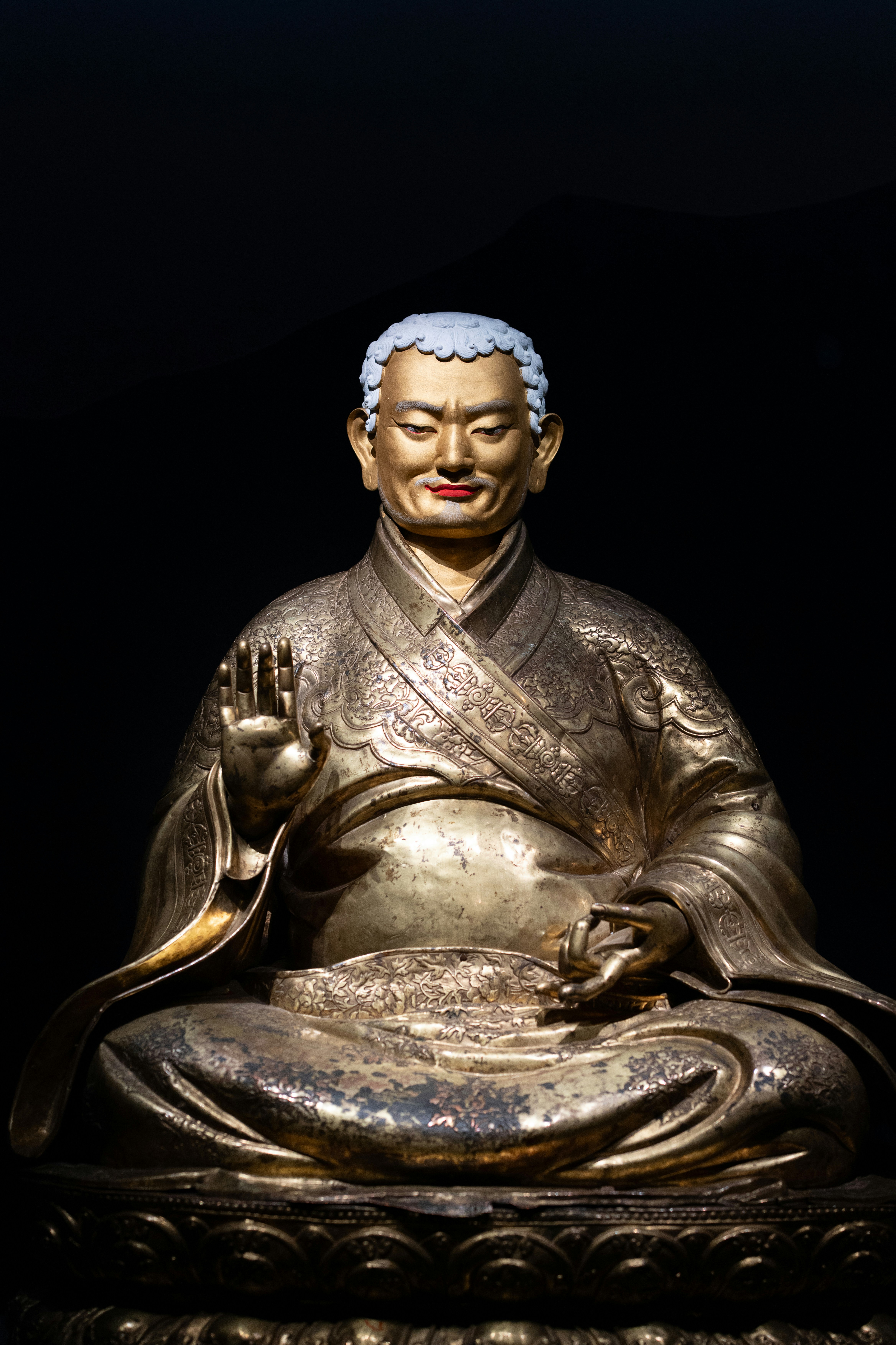 Midday stillness: a seated bronze Buddha with a raised right hand in a dim shrine