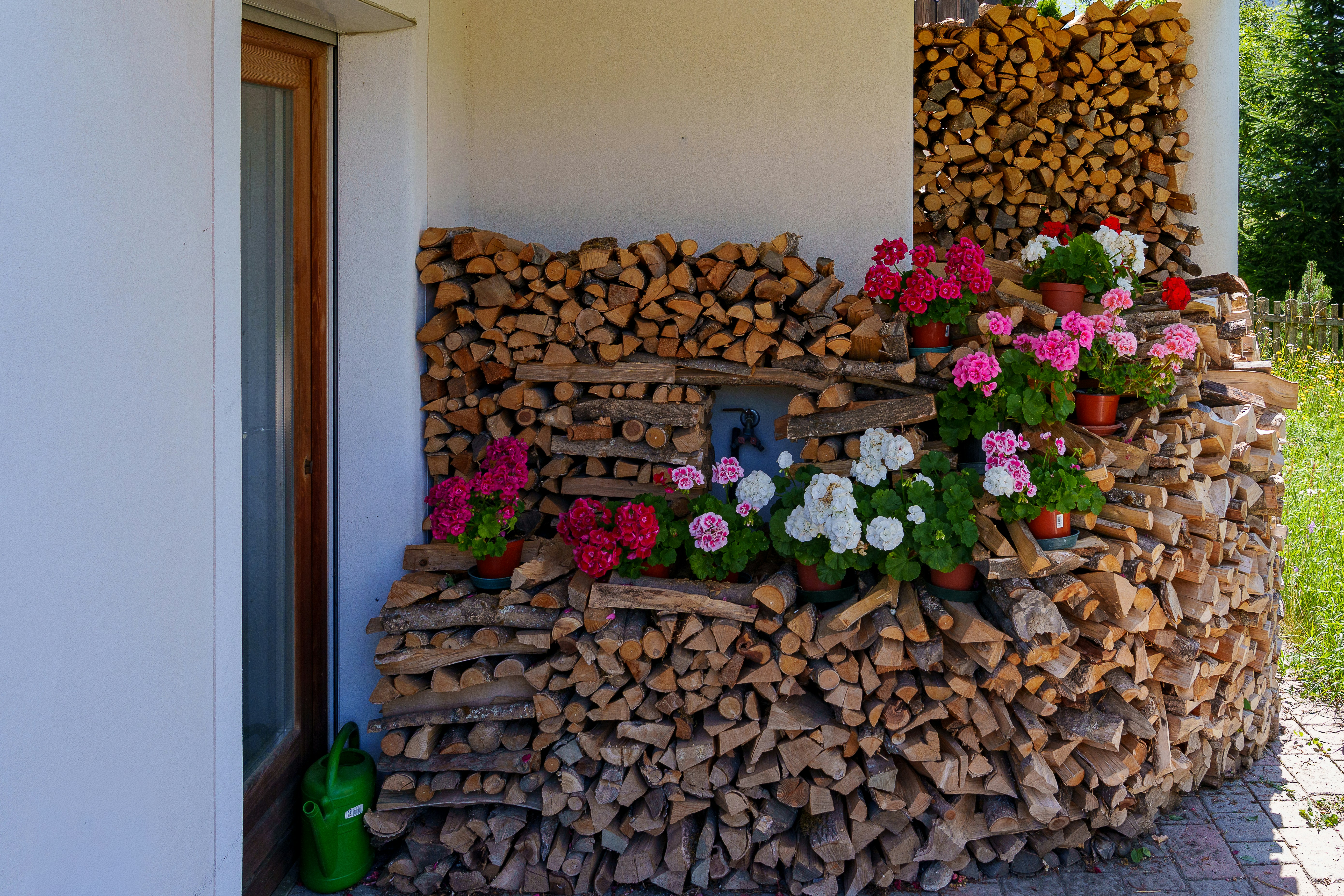 Clay-green Doorway Framed by Stacked Firewood and Flowers