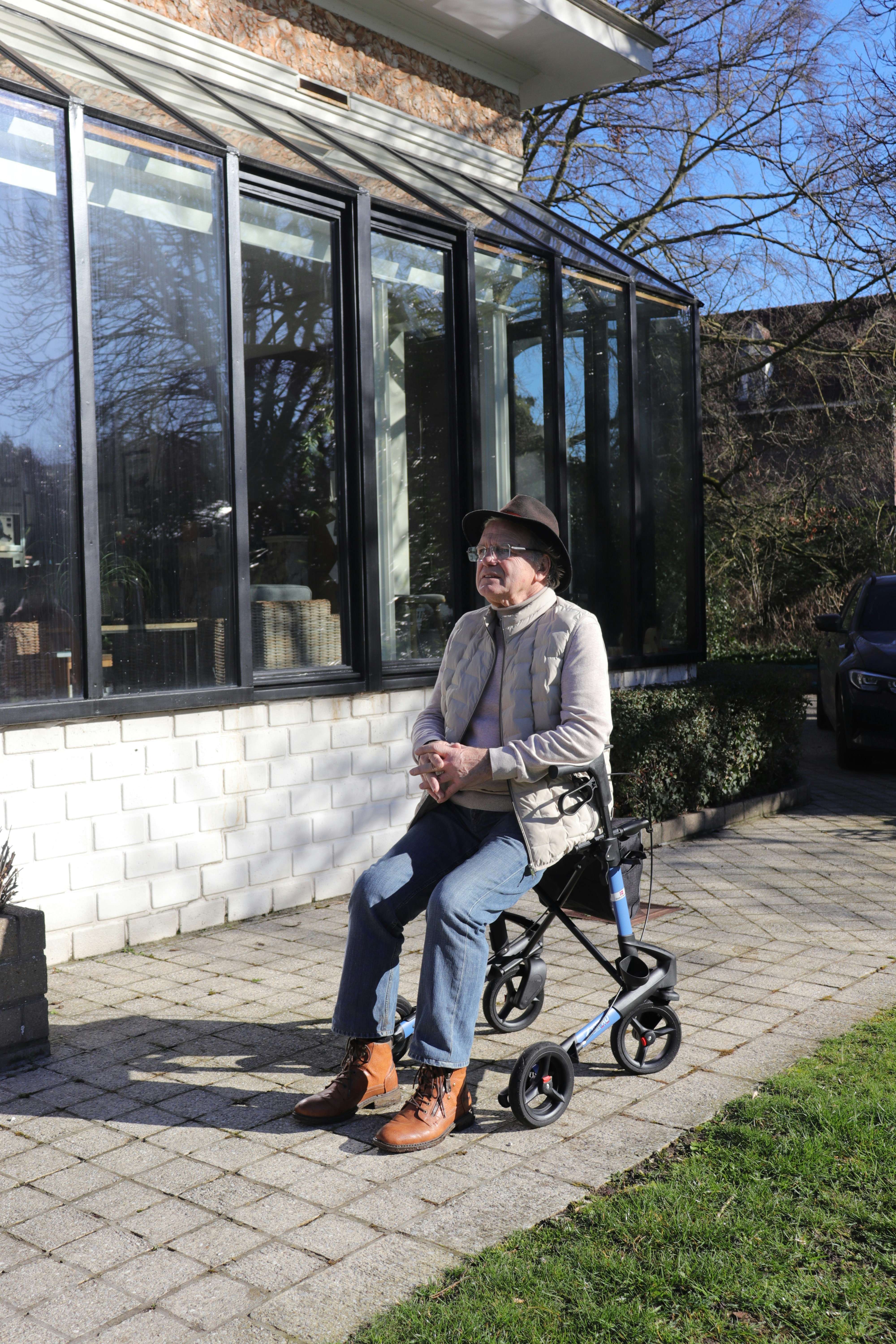 Elderly Gardener on a Mobility Walker Pauses by a Glass-Wreen Conservatory