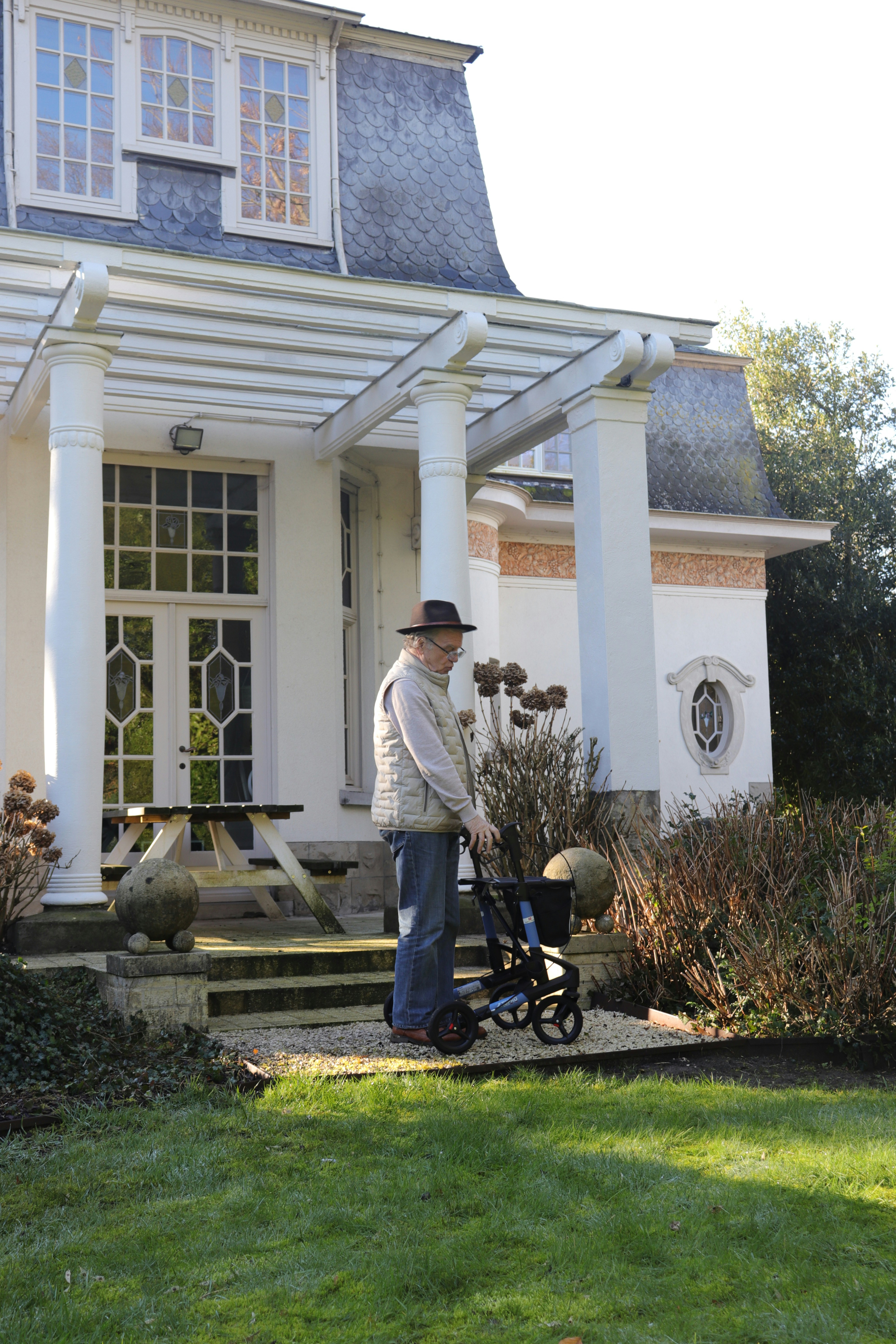 Gentleman with a walker at the porch of a stately white house