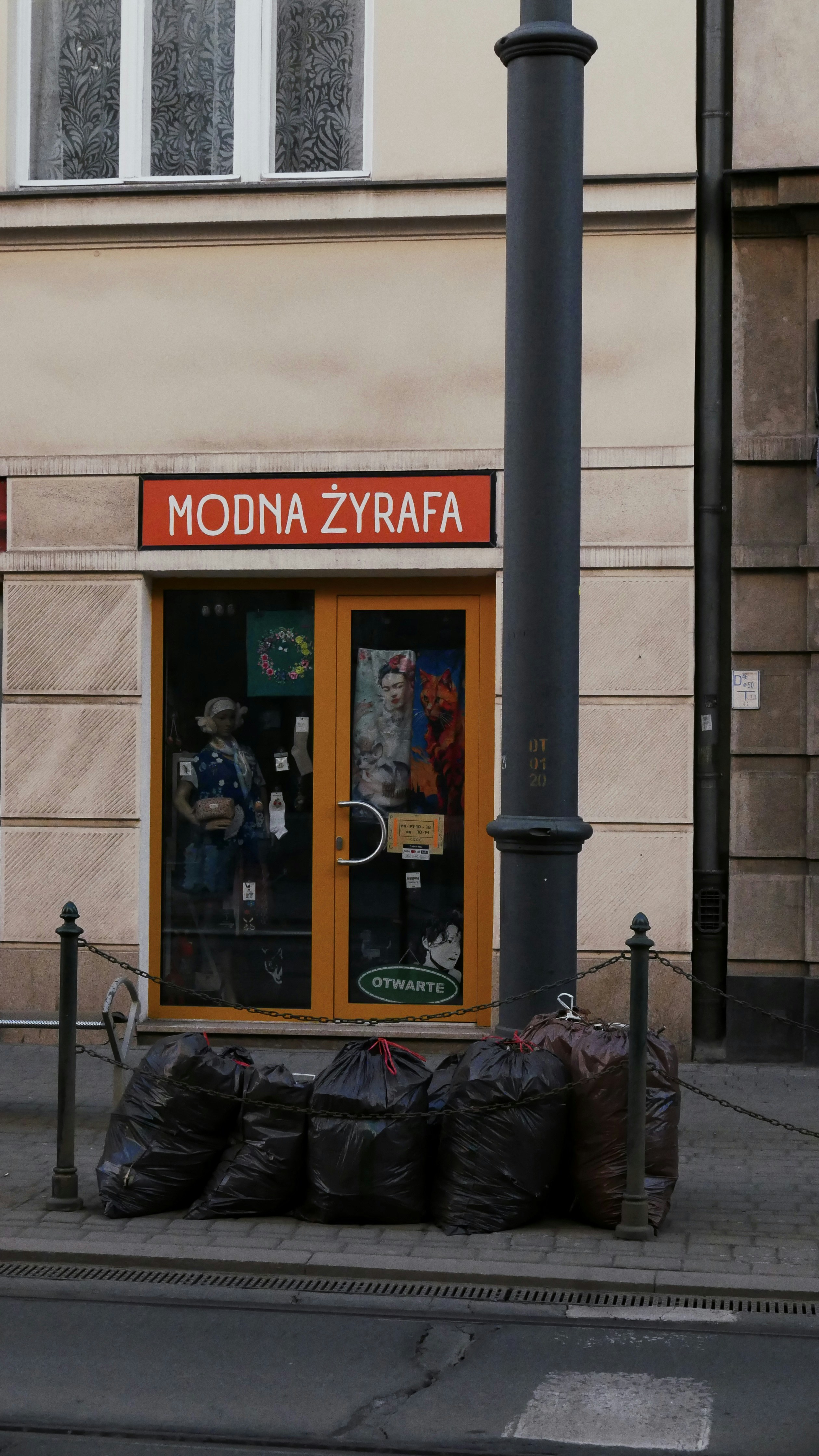 Bright orange-framed storefront with bold red sign and row of black garbage bags