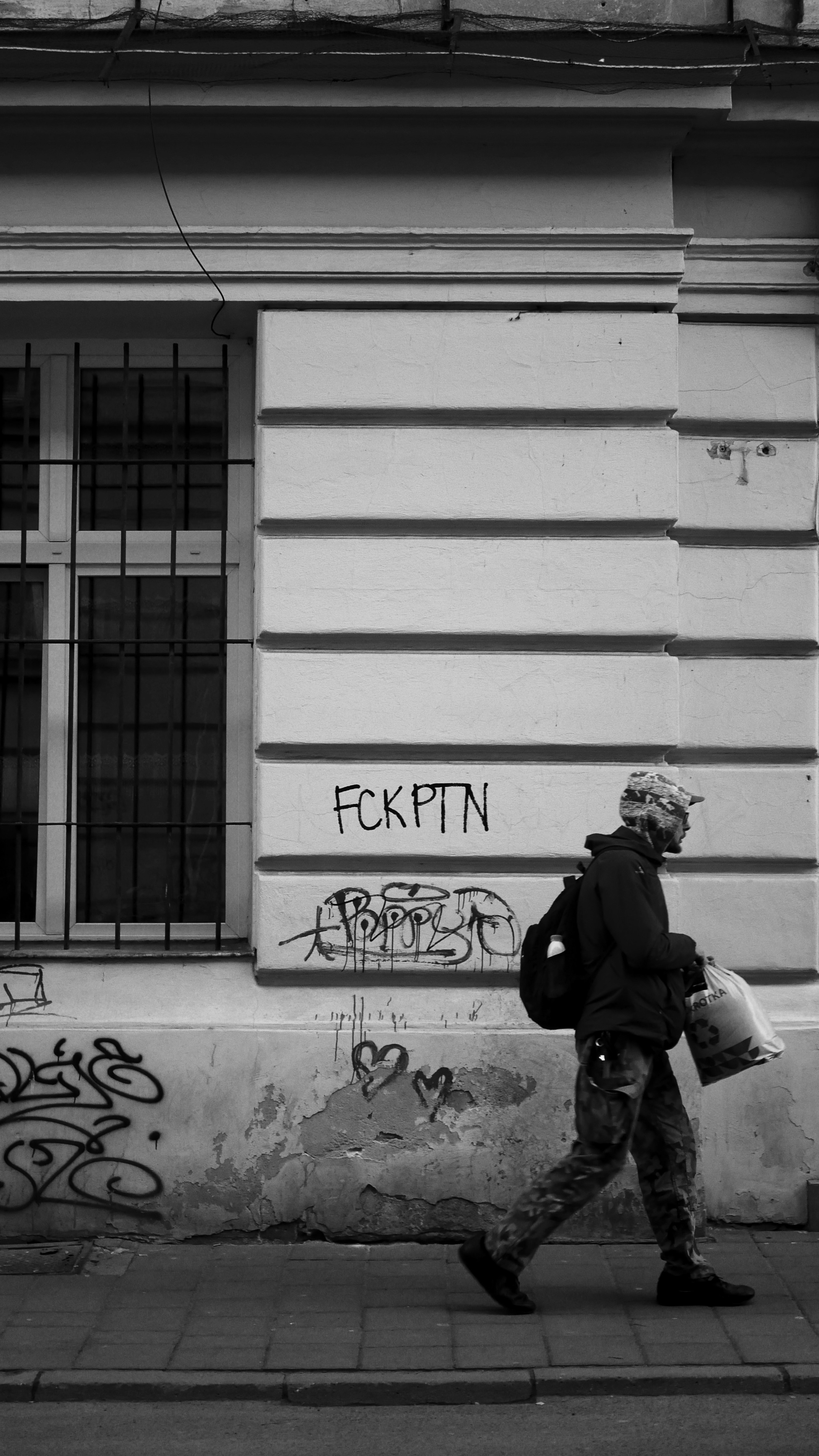 Pedestrian in shadowed street, graffiti walls and a lone traveler