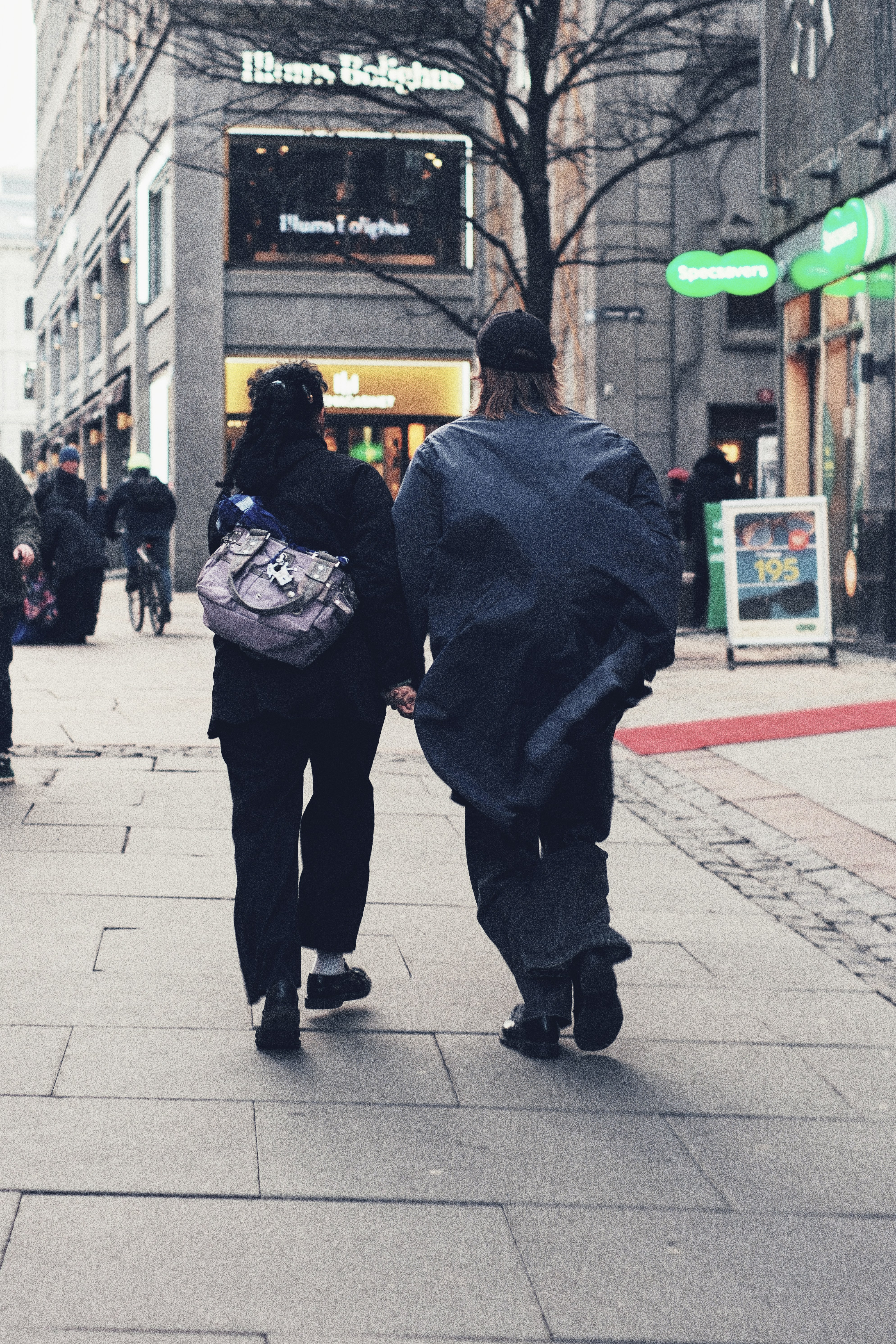 Two Friends Walk Arm in Arm Down a City Street