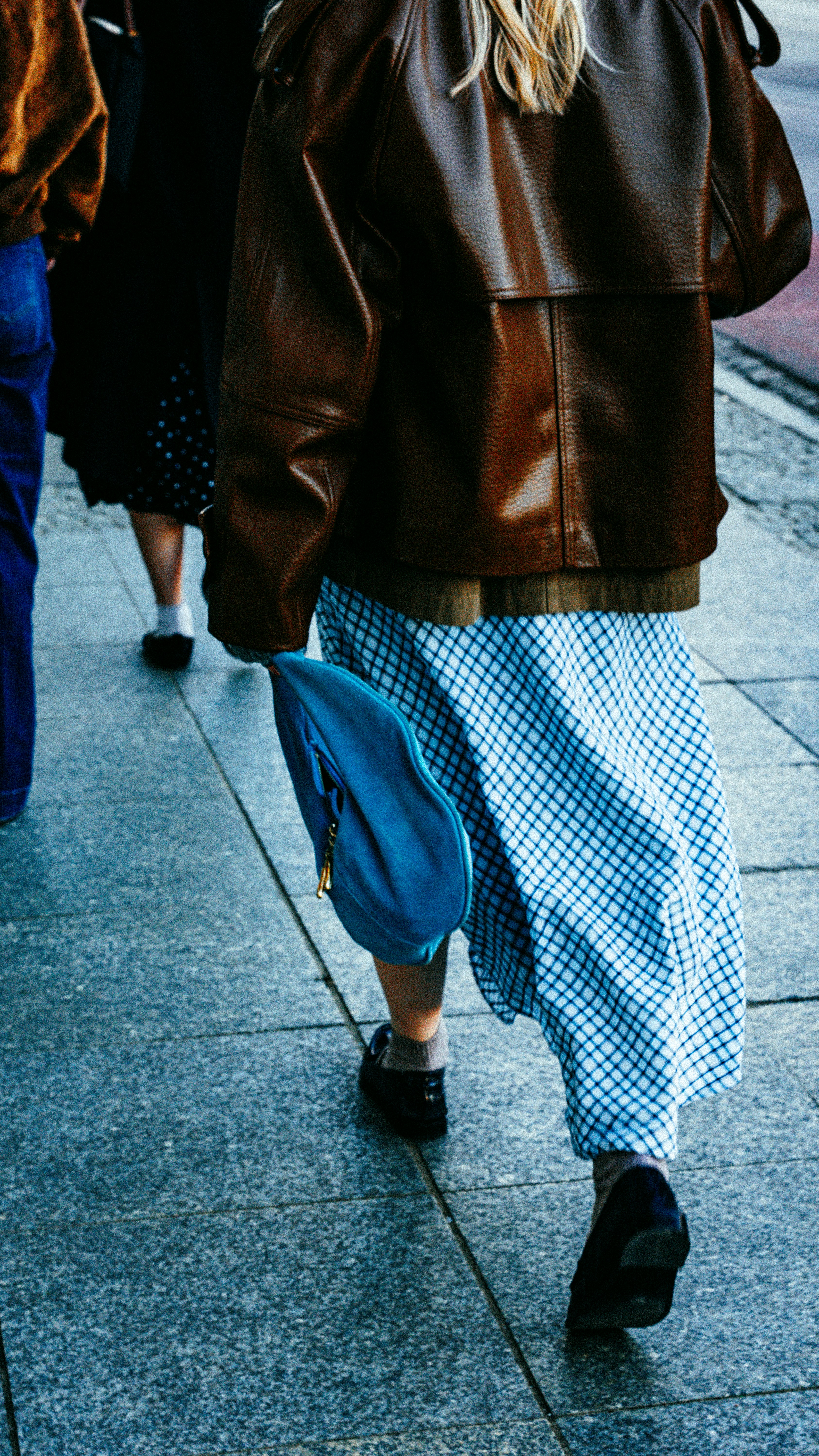 Blue clutch and leather jacket in motion on a city sidewalk