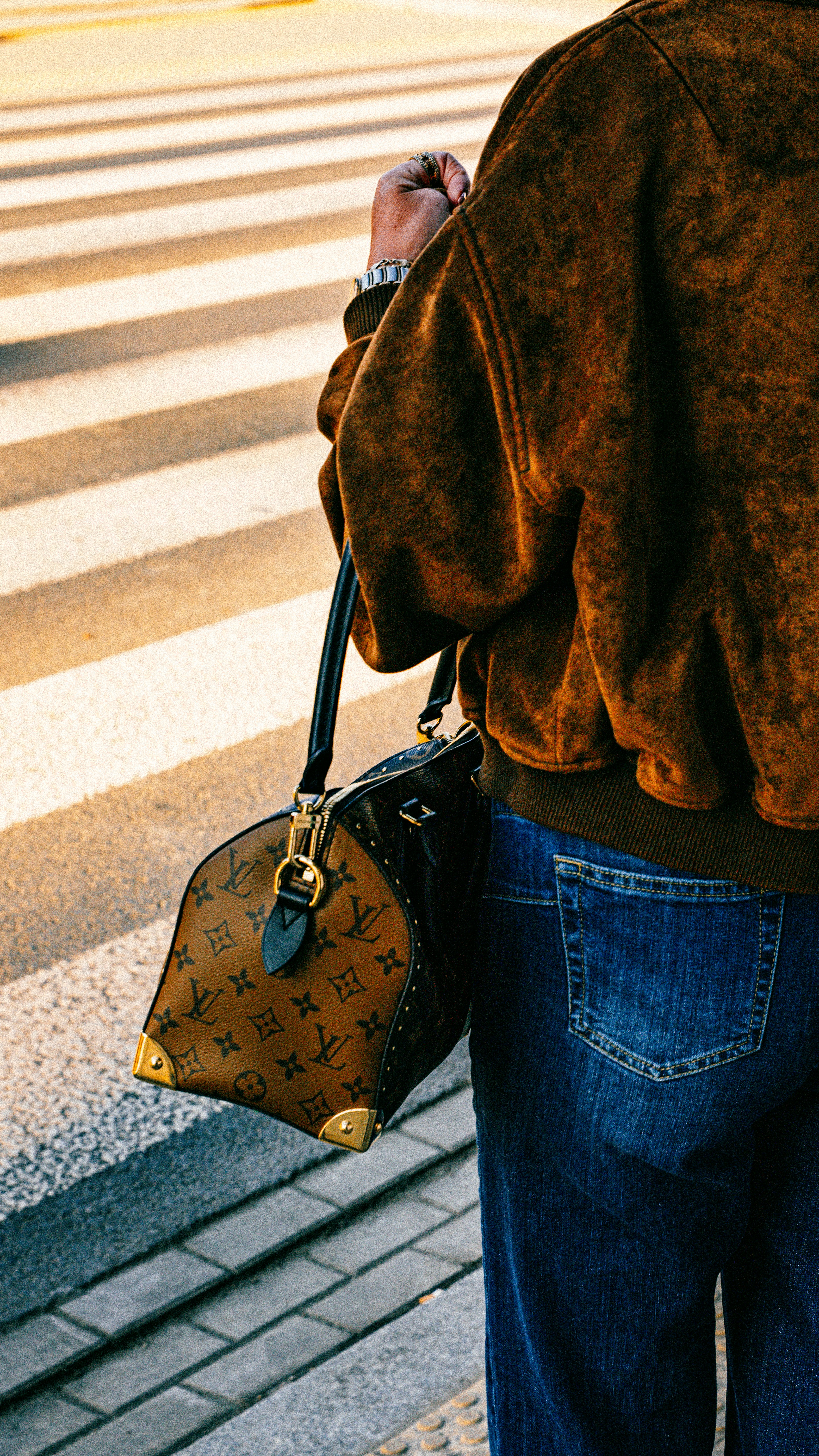 Brown suede jacket, blue jeans, and a Louis Vuitton handbag in urban street light glow