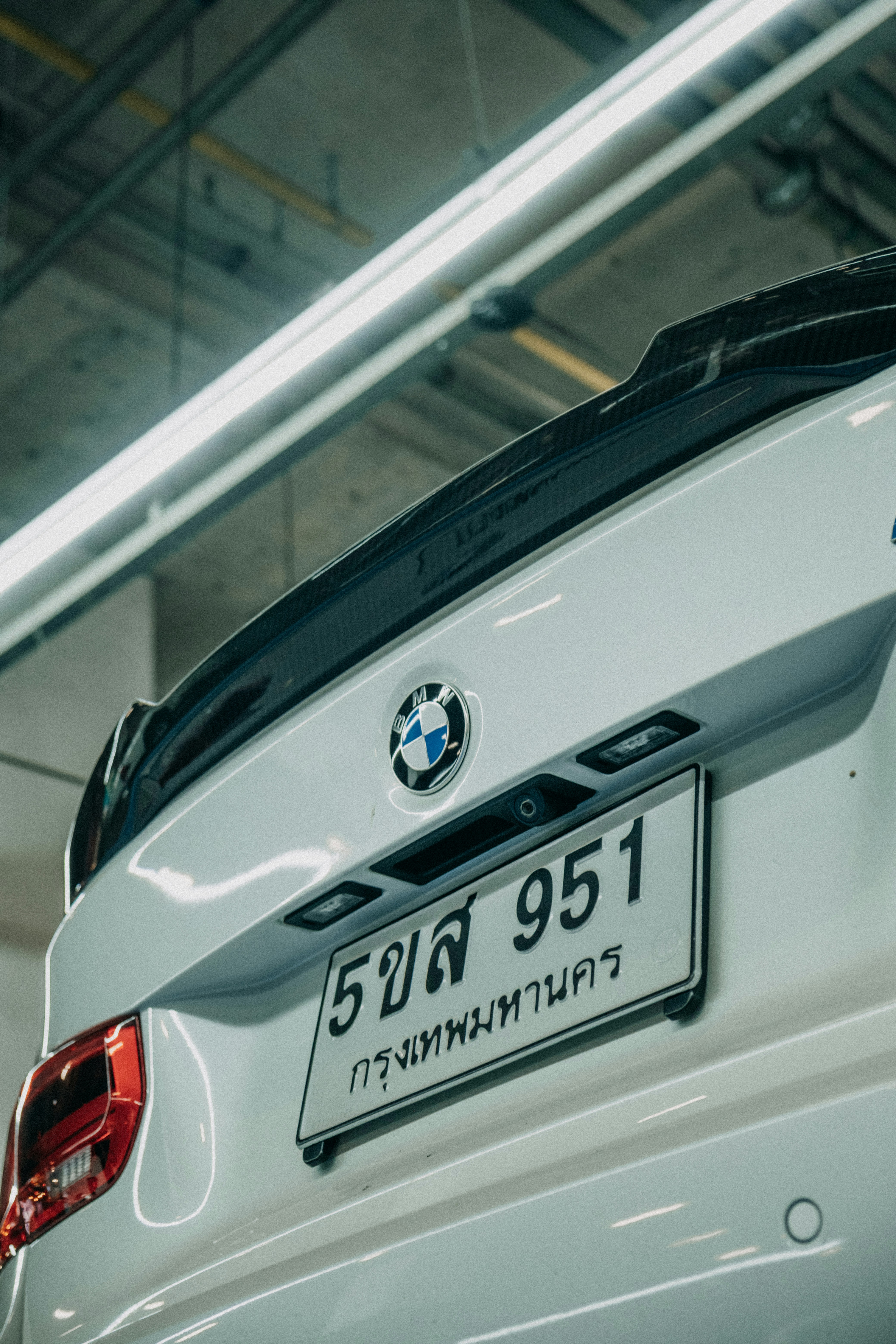 Rear-view of a white BMW in a dim auto workshop with Thai license plate